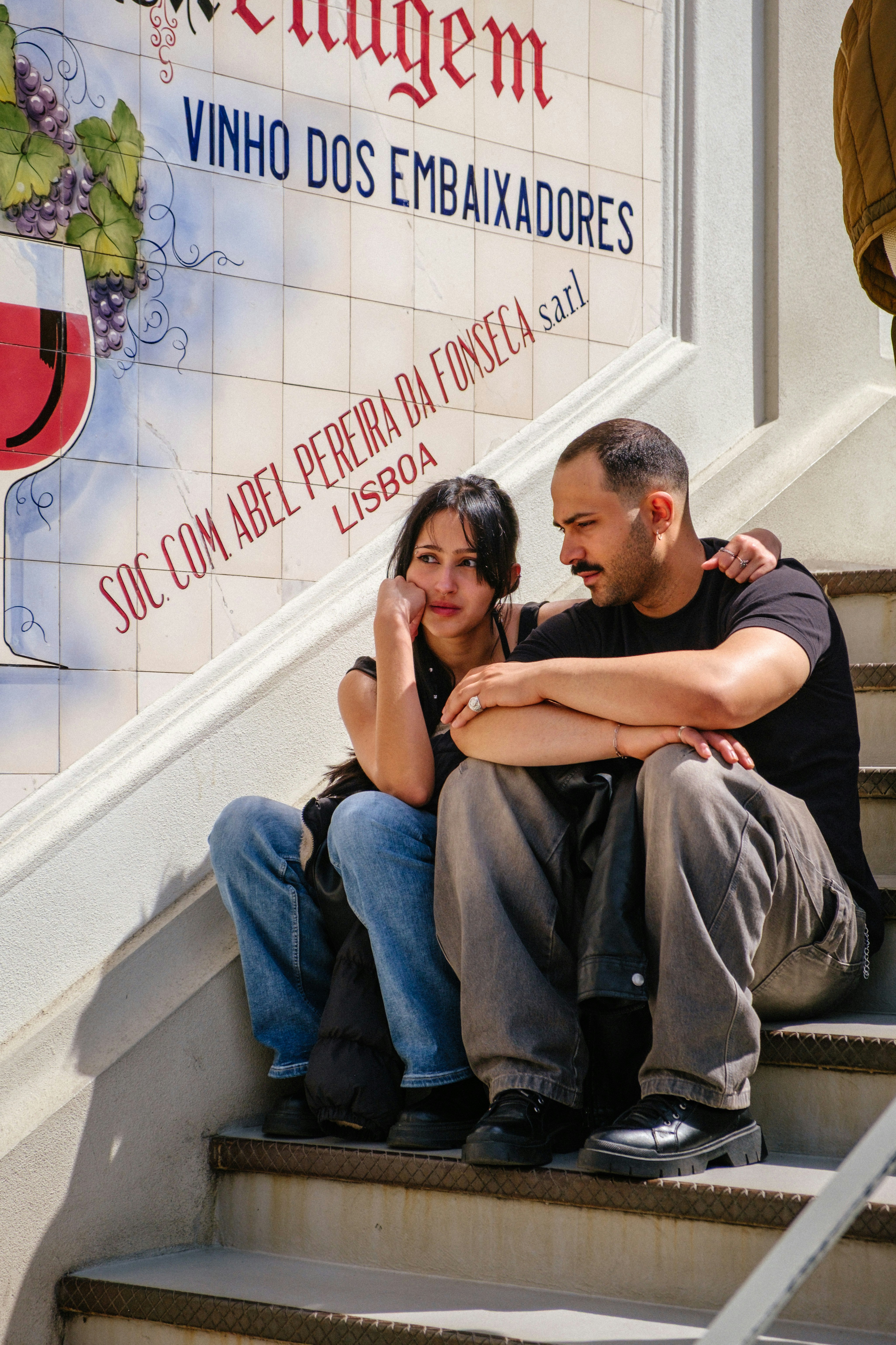 Couple on the stairs under a tiled mural, daylight and quiet conversation