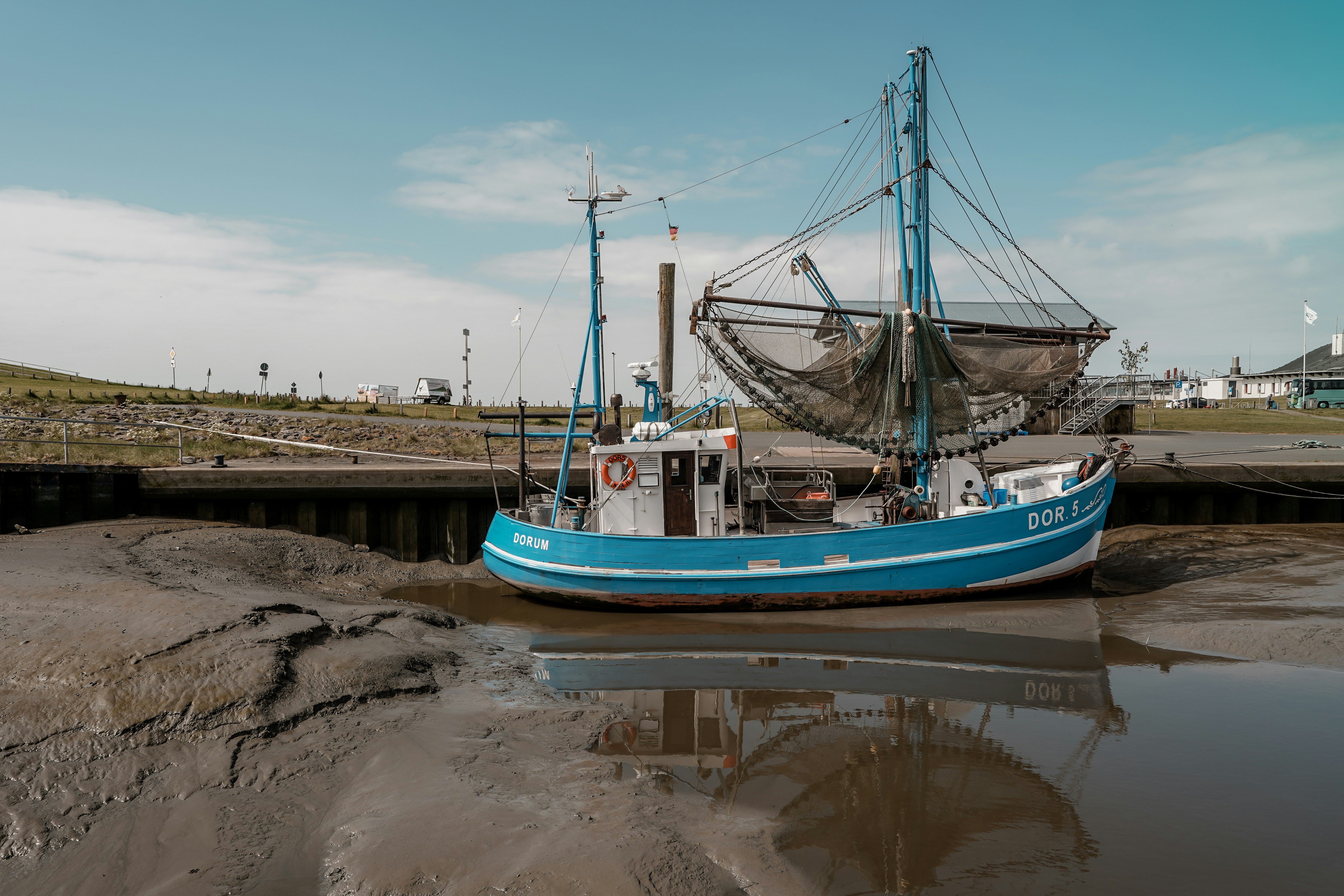 Blue fishing boat at low-tide harbor with net crane