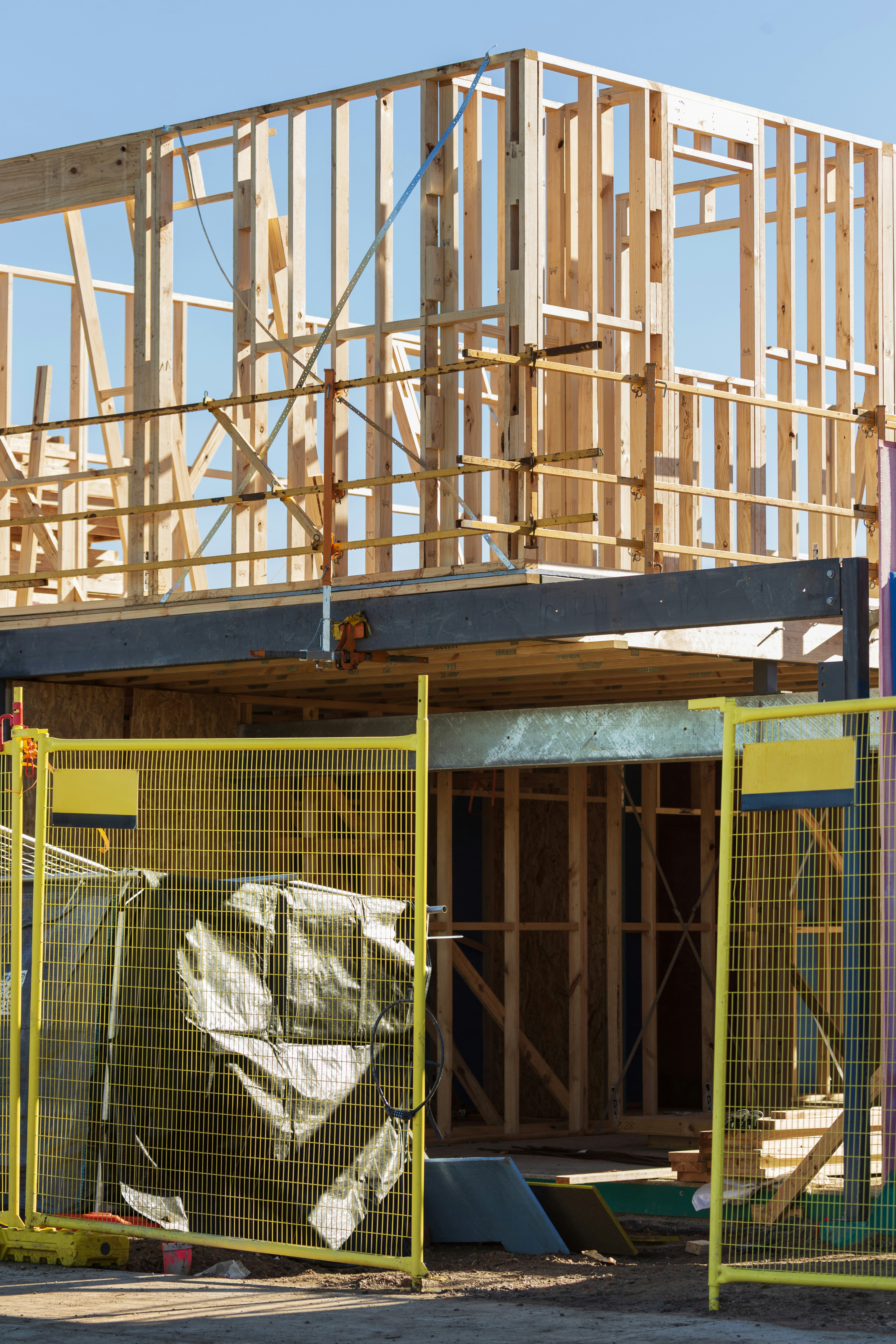 Framing the Frame: Wooden Skeleton of a Construction Site Emerges Behind Yellow Barriers