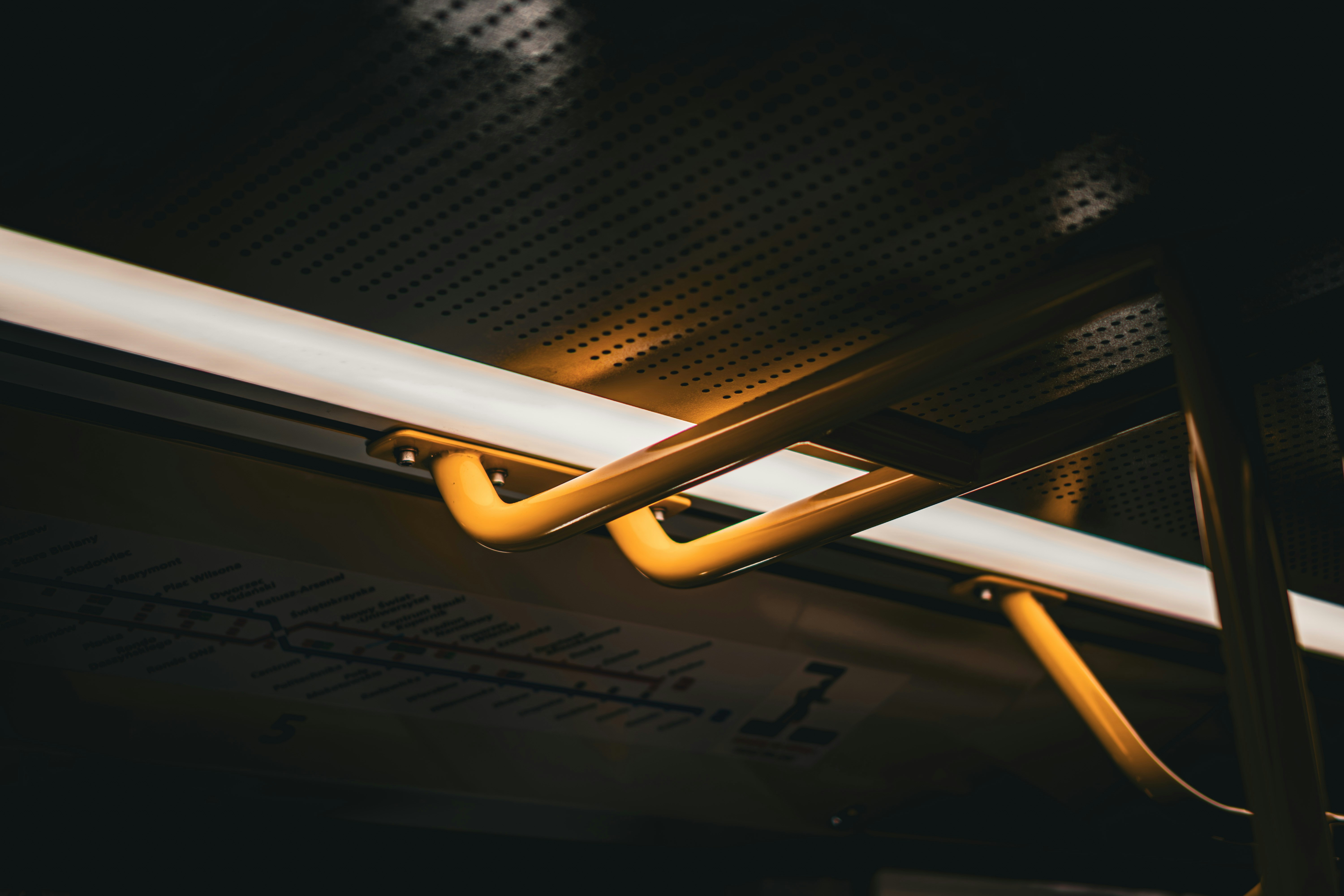 Dimly lit interior with warm-toned metal handrails and overhead piping inside a subway or train car.
