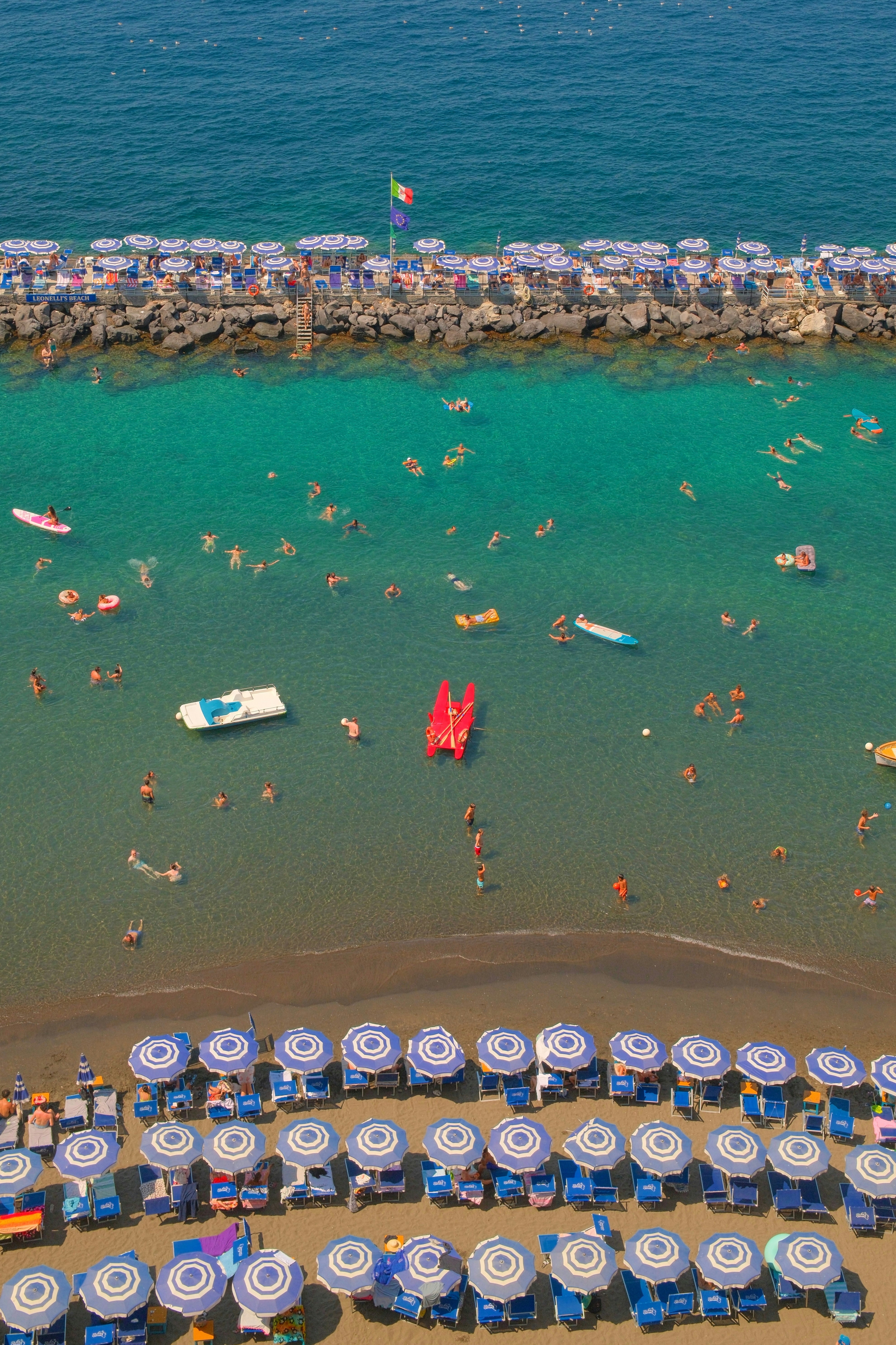 Sunlit Umbrellas, Turquoise Waters, and a Bustle Along the Beach Breakwater