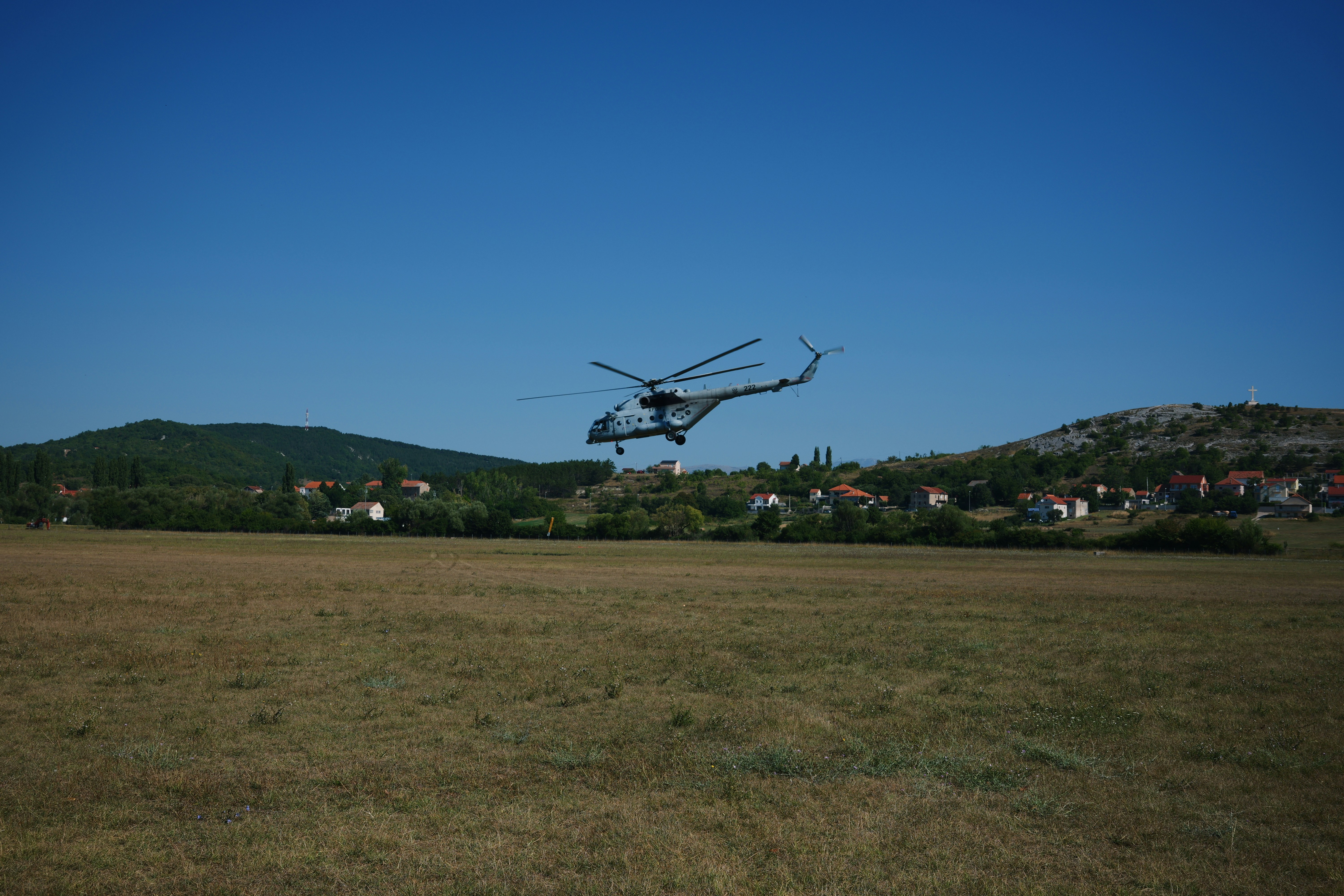 Midair Helix: A helicopter hovers over a sunlit field toward a distant village