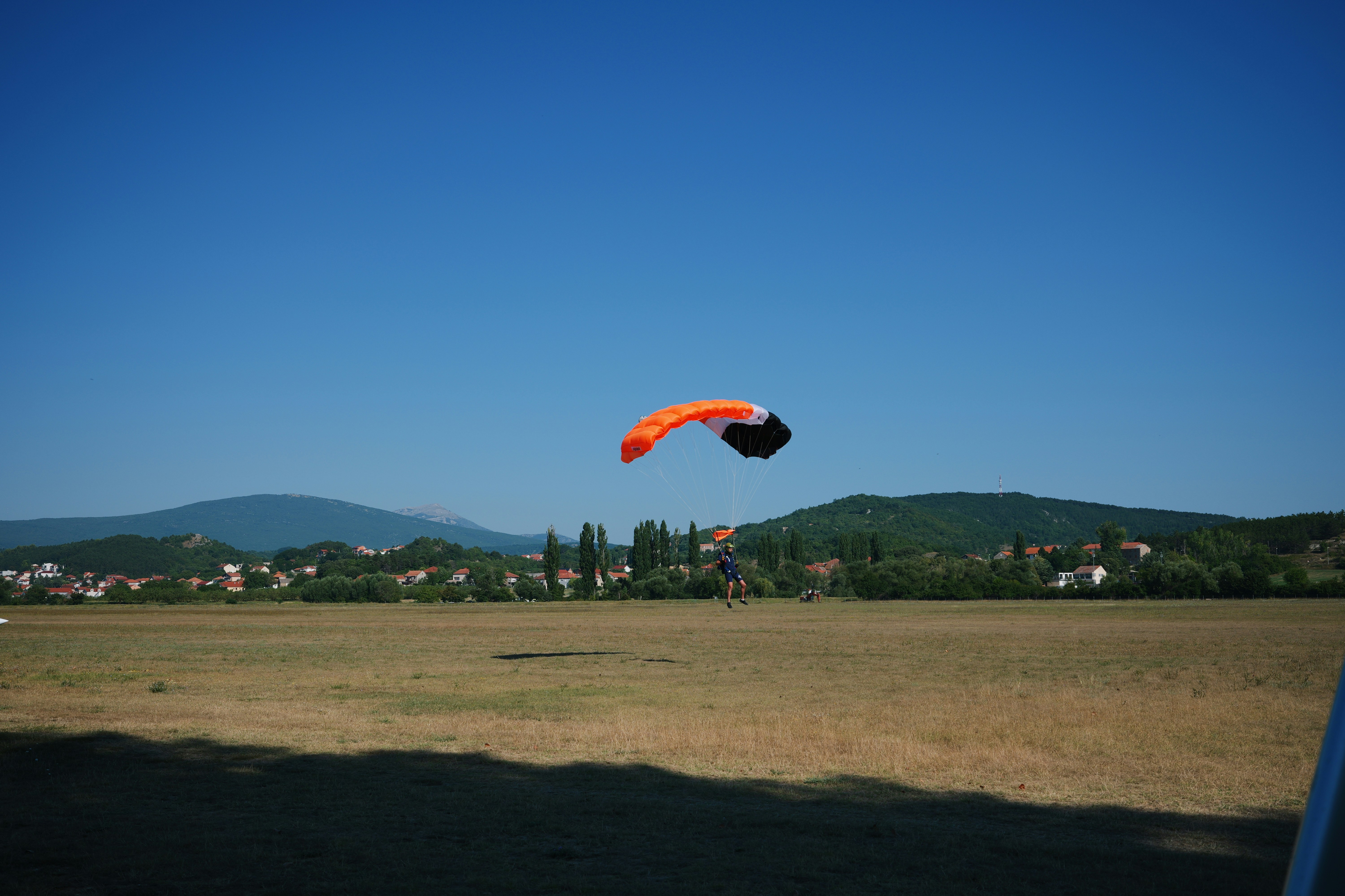 Midfield Jump: A Paraglider Leaps Above an Open Field Under a Clear Blue Sky