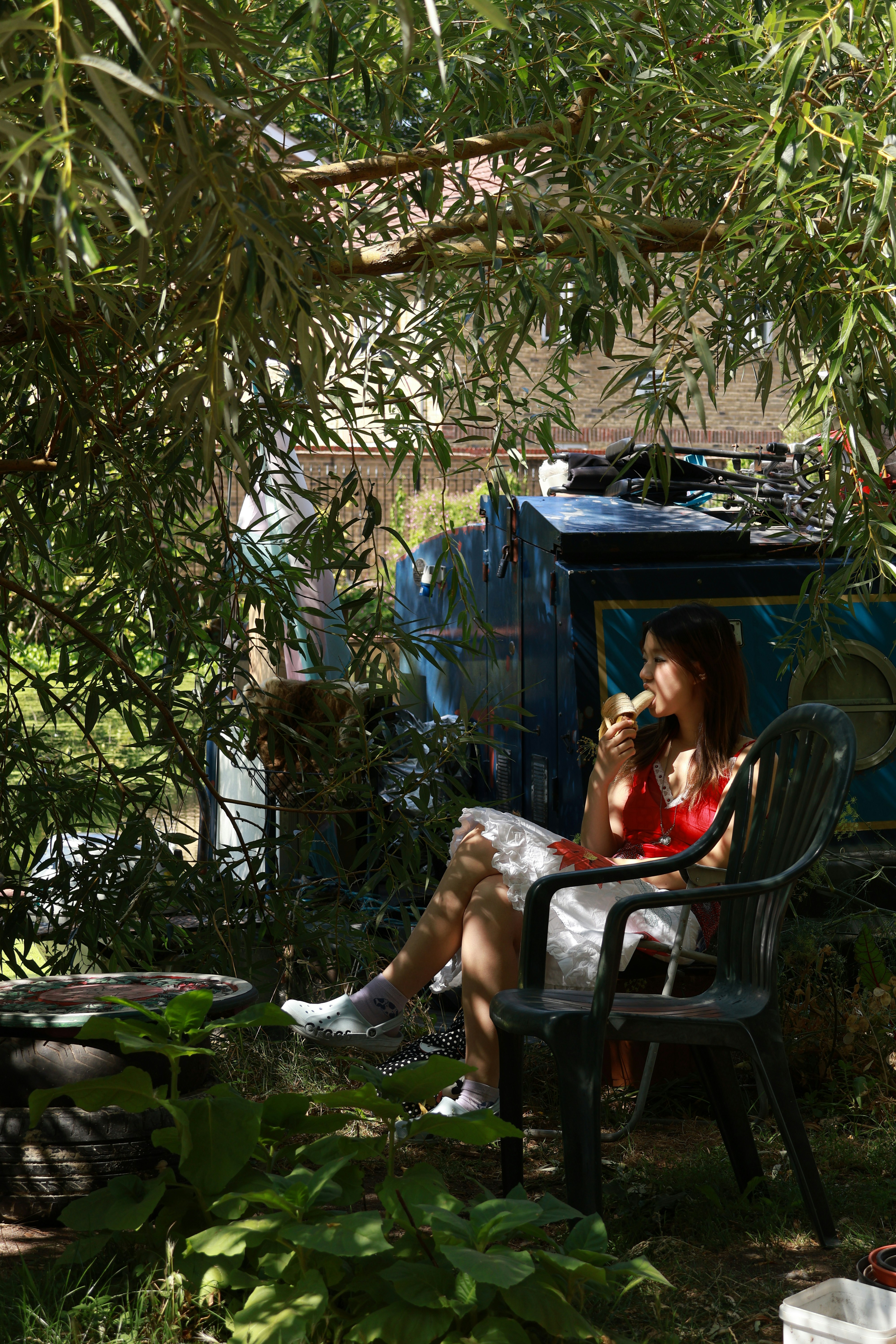 Sunlit Moment: A Woman Relaxing with Ice Cream by the Garden Tree