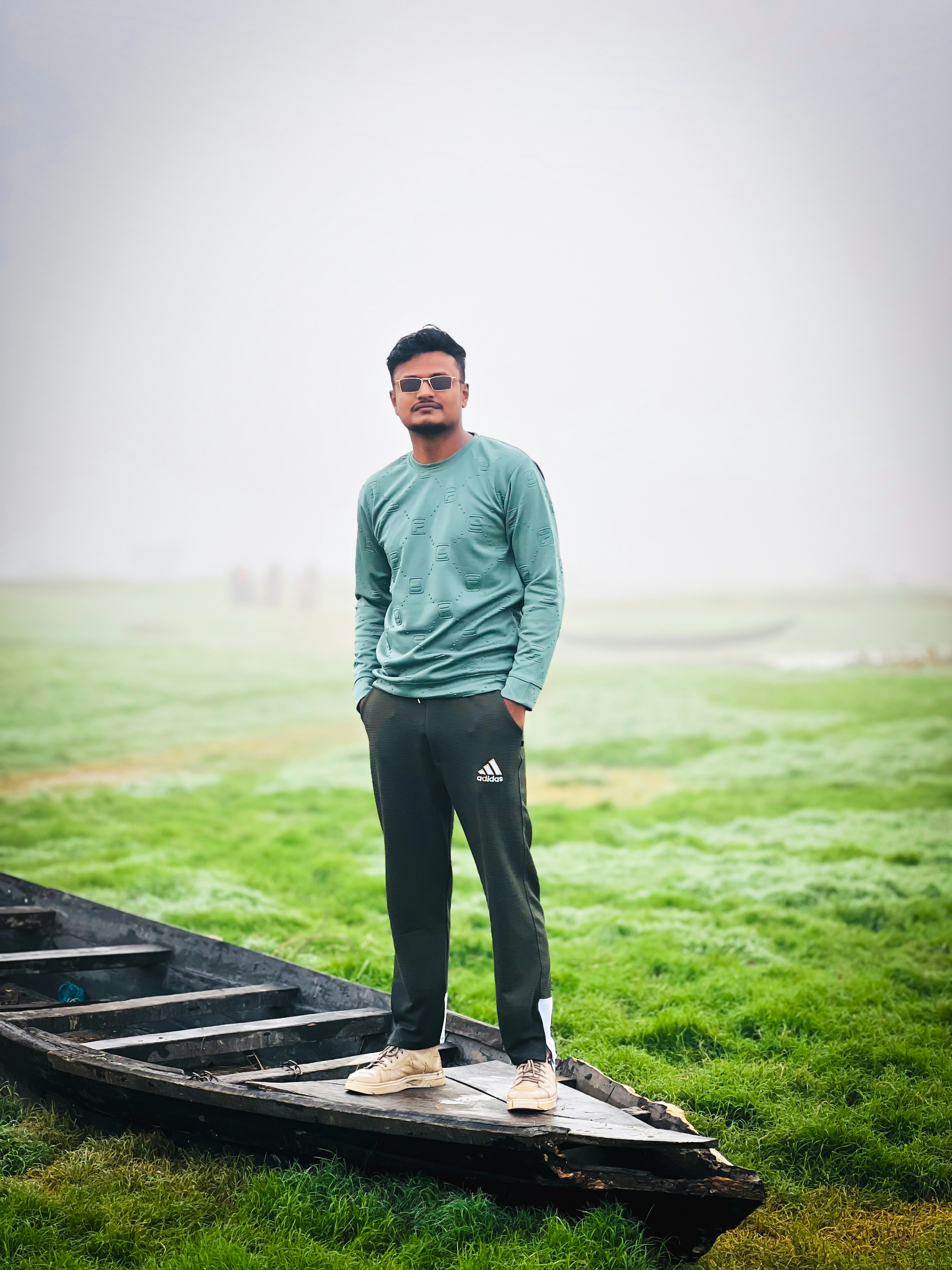 Man in teal sweatshirt standing on an old wooden boat in a foggy field