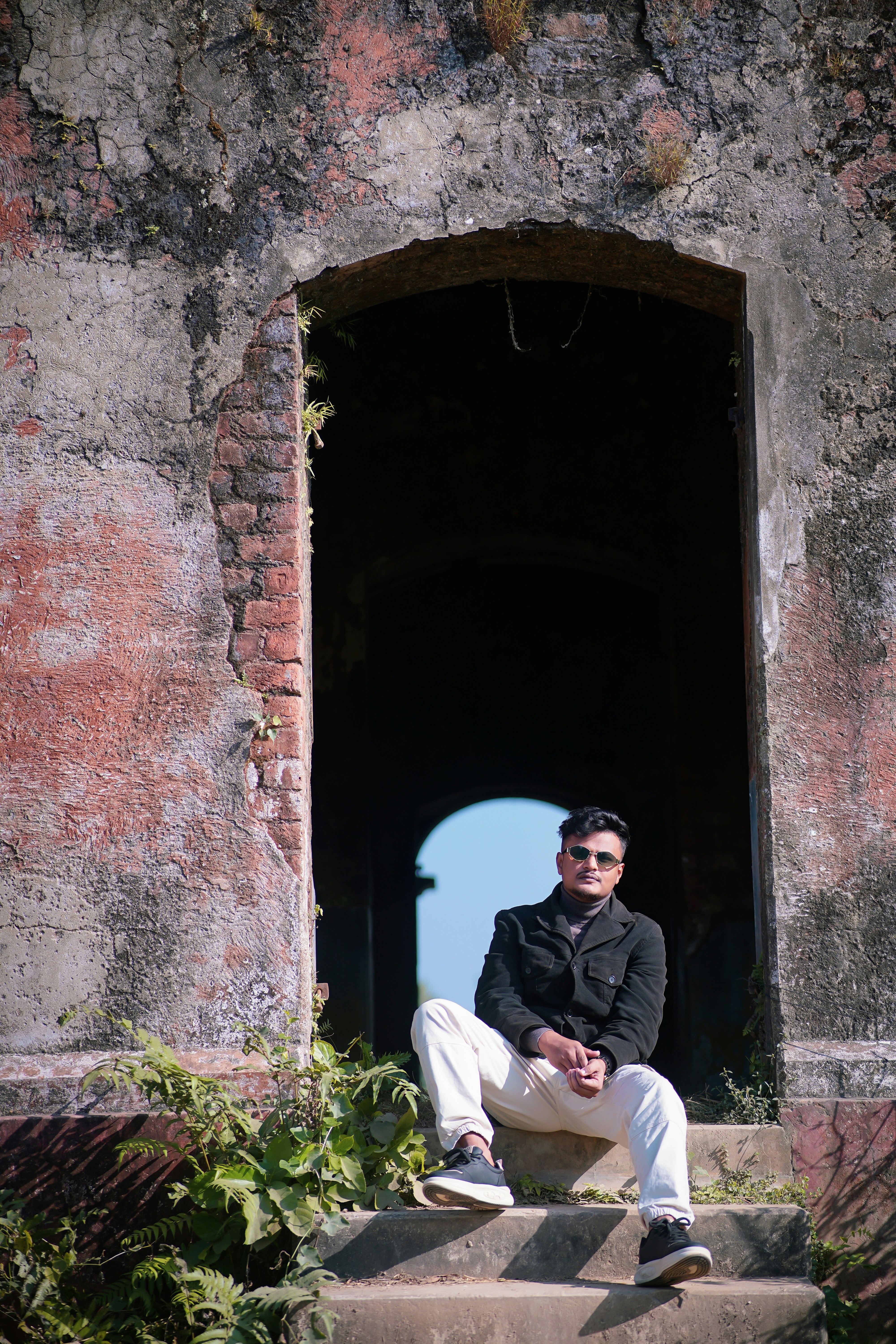 Man in sunglasses seated at the threshold of an ancient archway