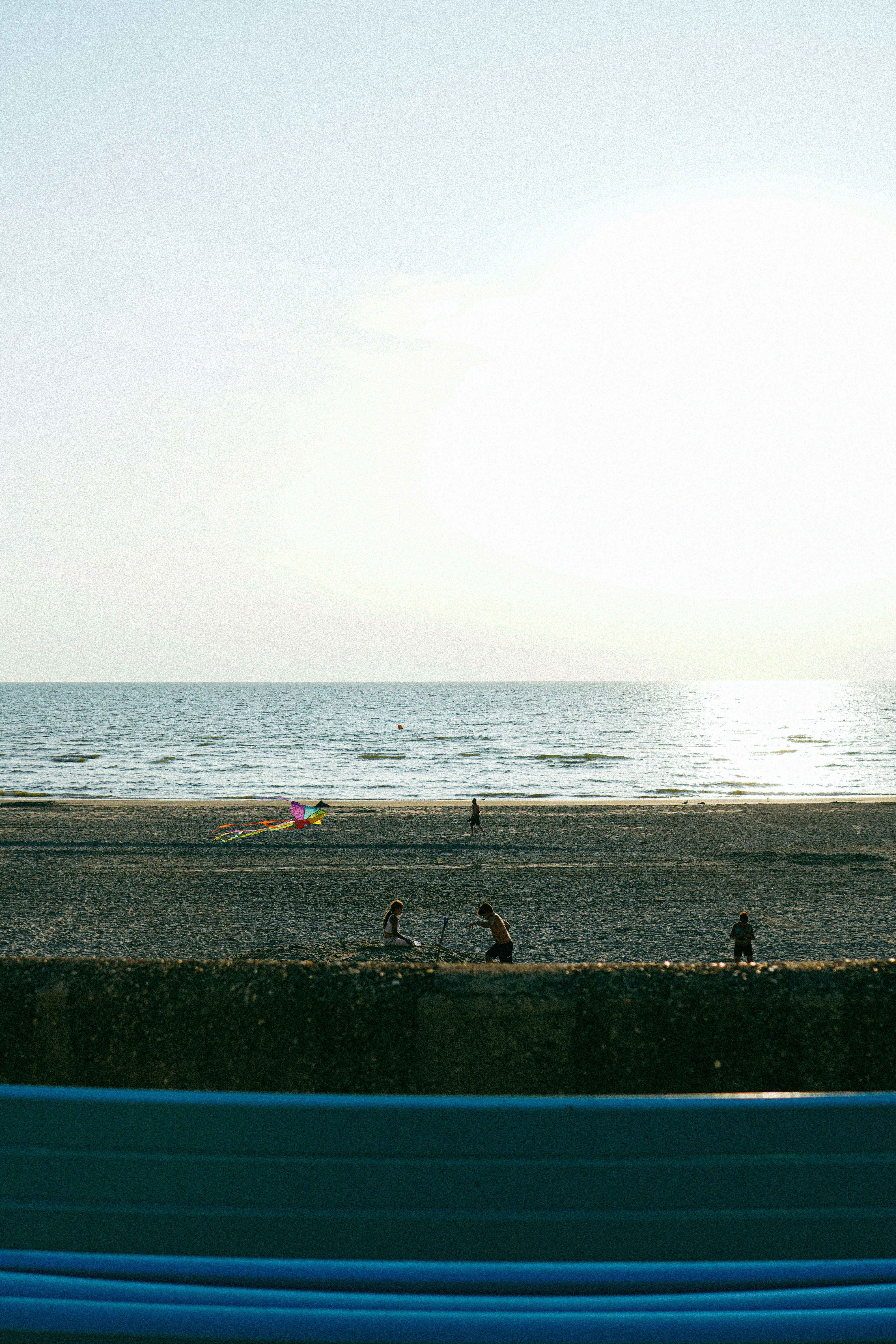 Sunlit Beach Quiet with Distant Figures and Blue Barrier