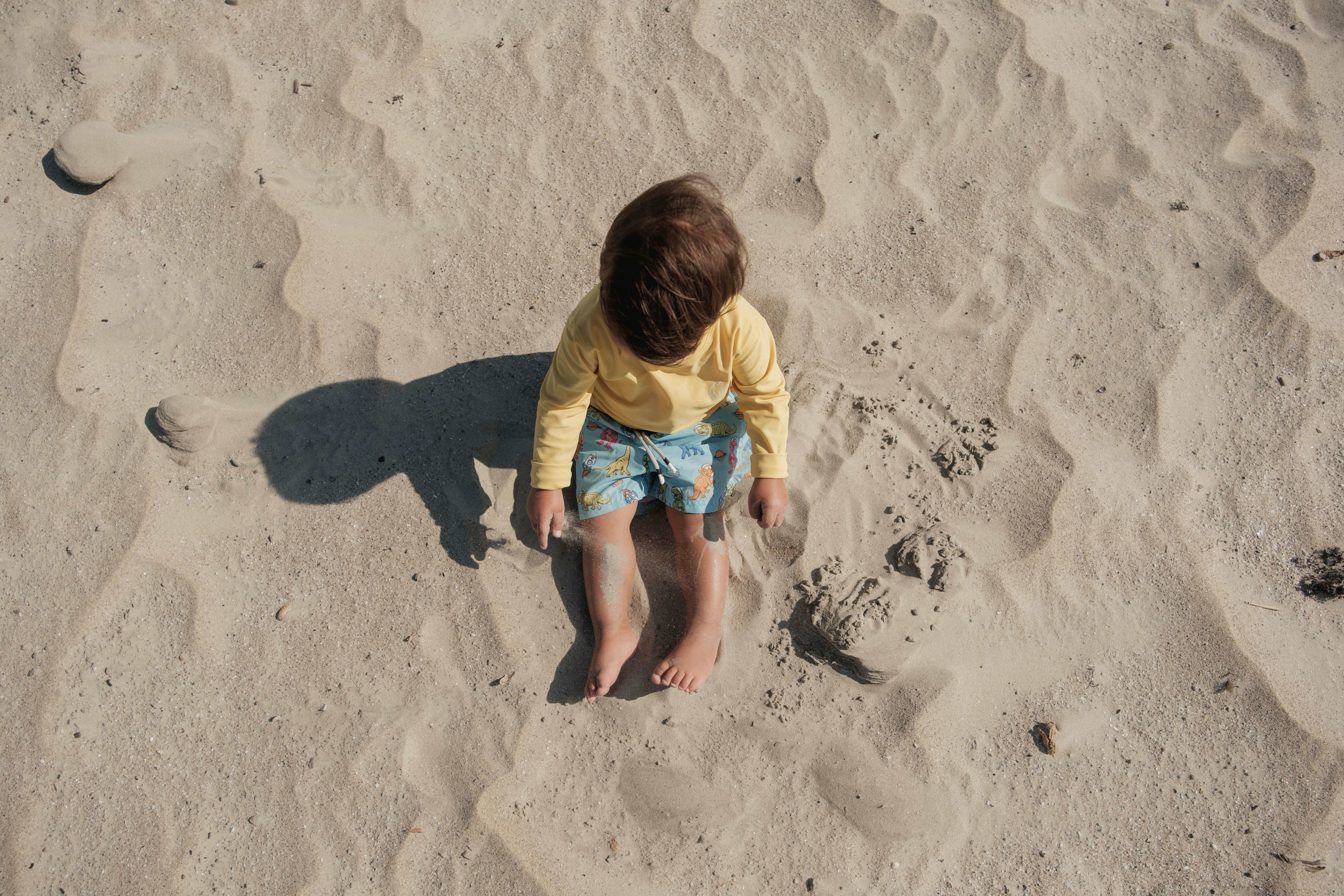 Child on sunlit sand: a quiet moment framed by footprints and wind-carved dunes