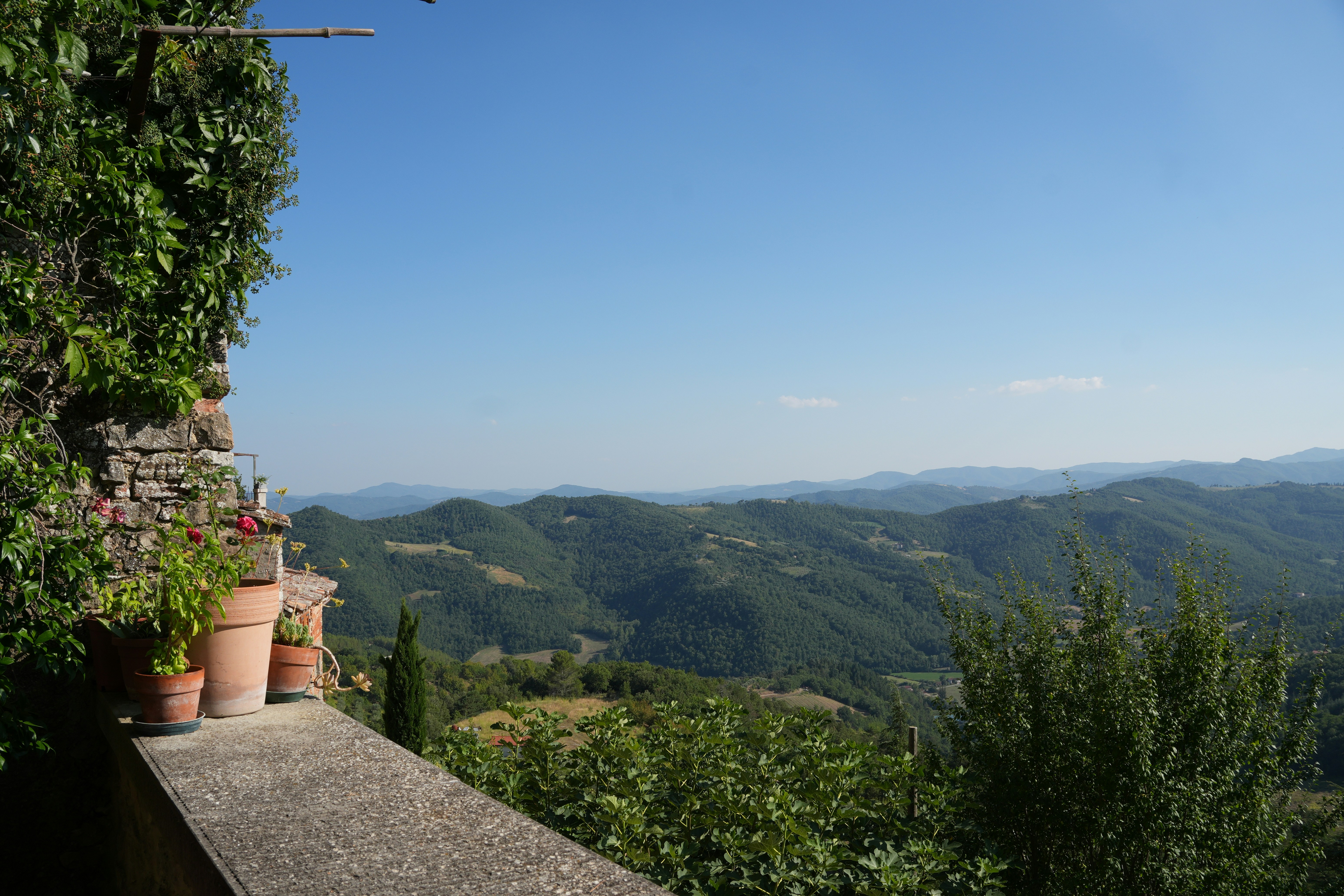 Terraced balconies with potted plants overlook winding Tuscan hills