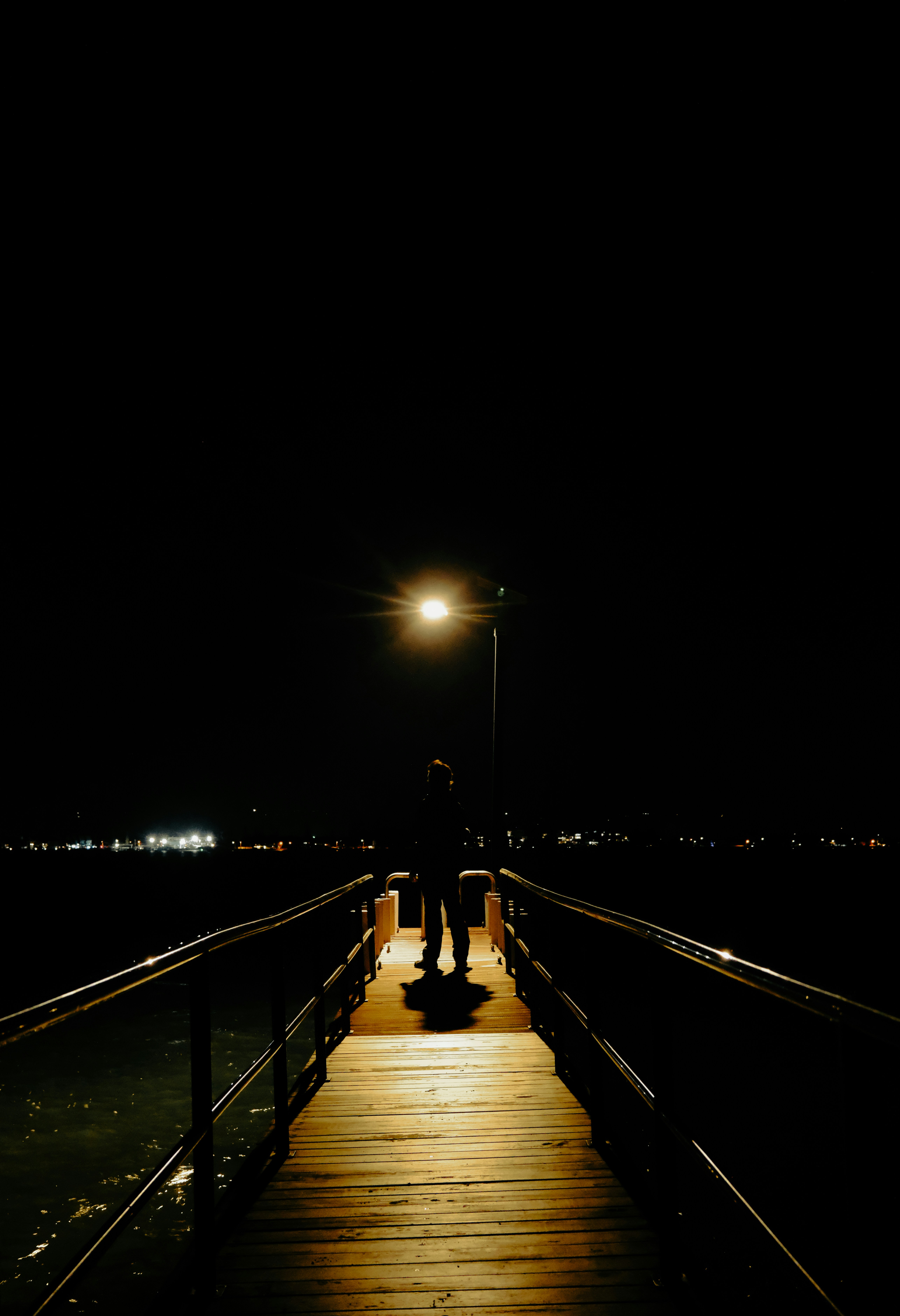 Night Pier Sentinel: A lone figure under a lamp on a quiet dock