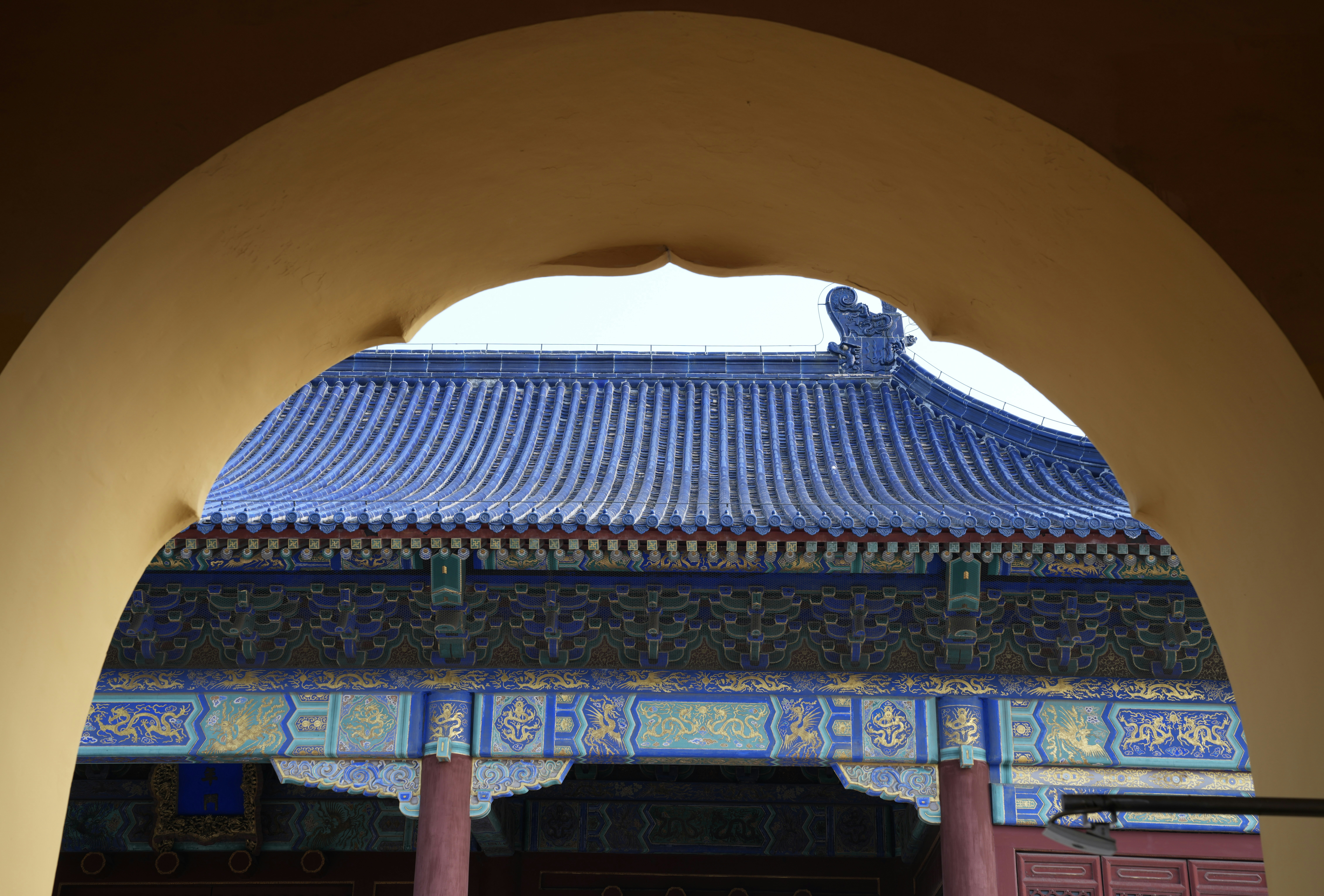 A traditionally painted arch frames the ornate eaves of a temple with blue and gold detailing visible beyond.