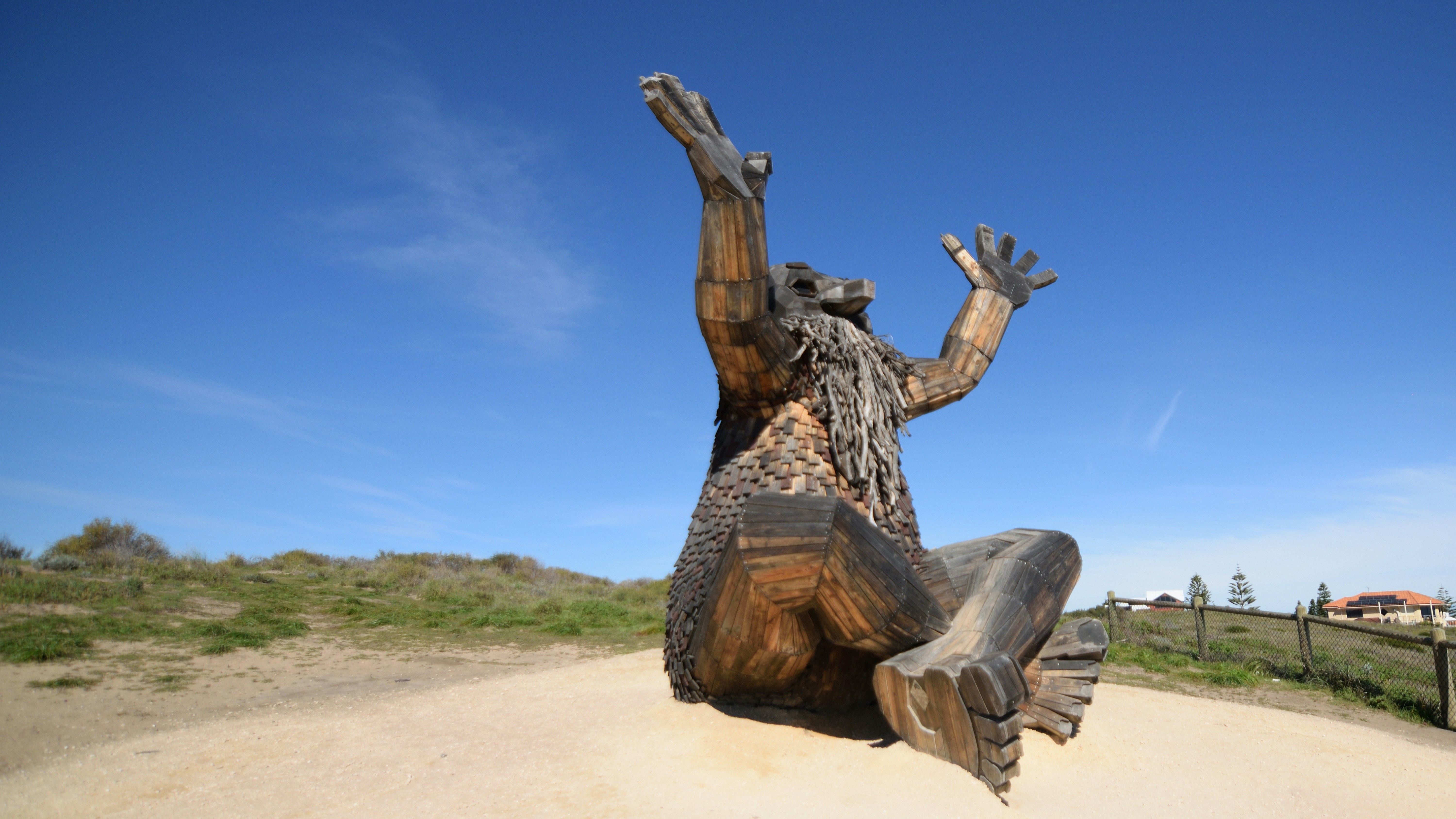 Giant wooden figure emerges from the dune under a clear coastal sky