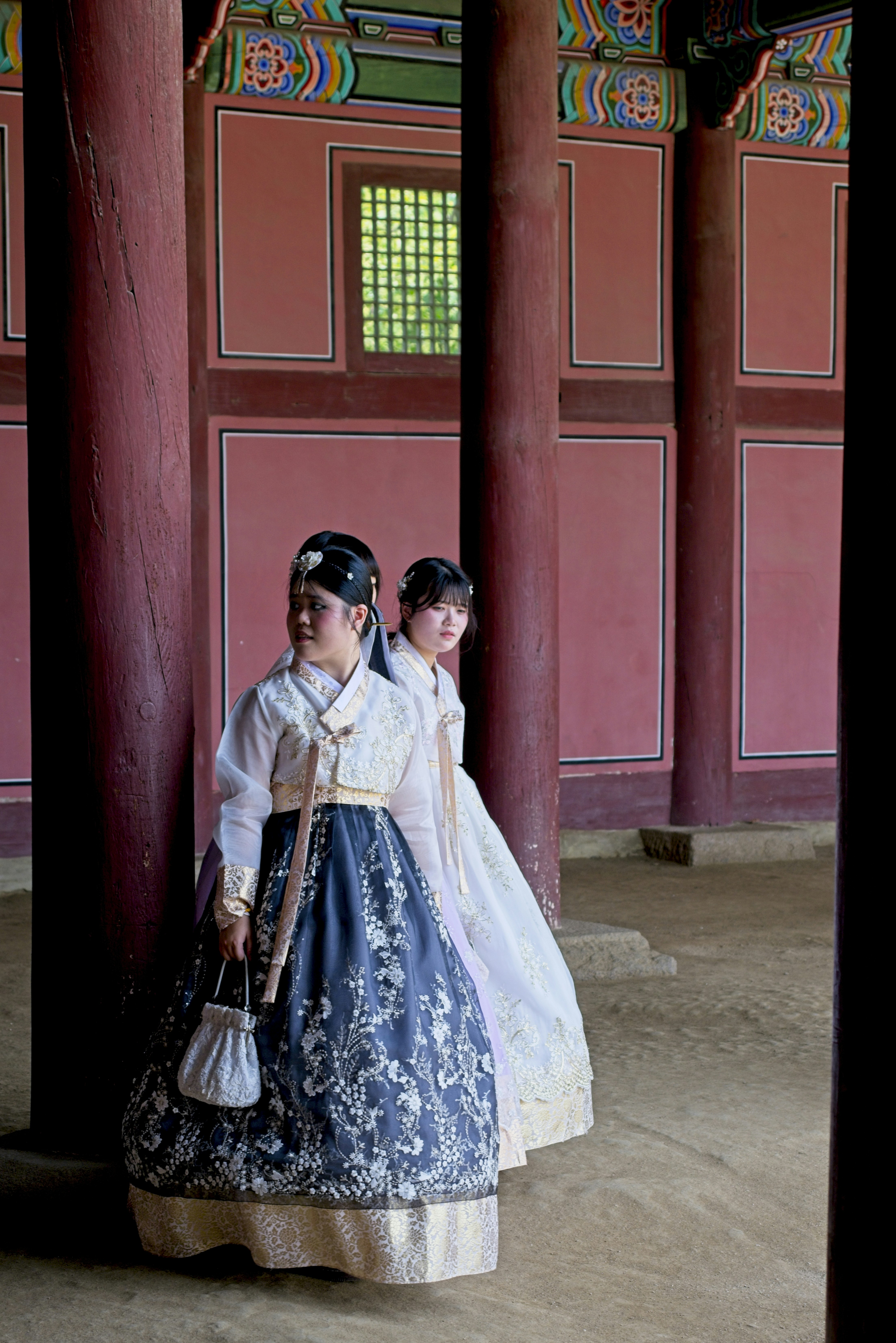 Dual silhouettes in a traditional courtyard: Hanbok ensembles framed by lacquered columns