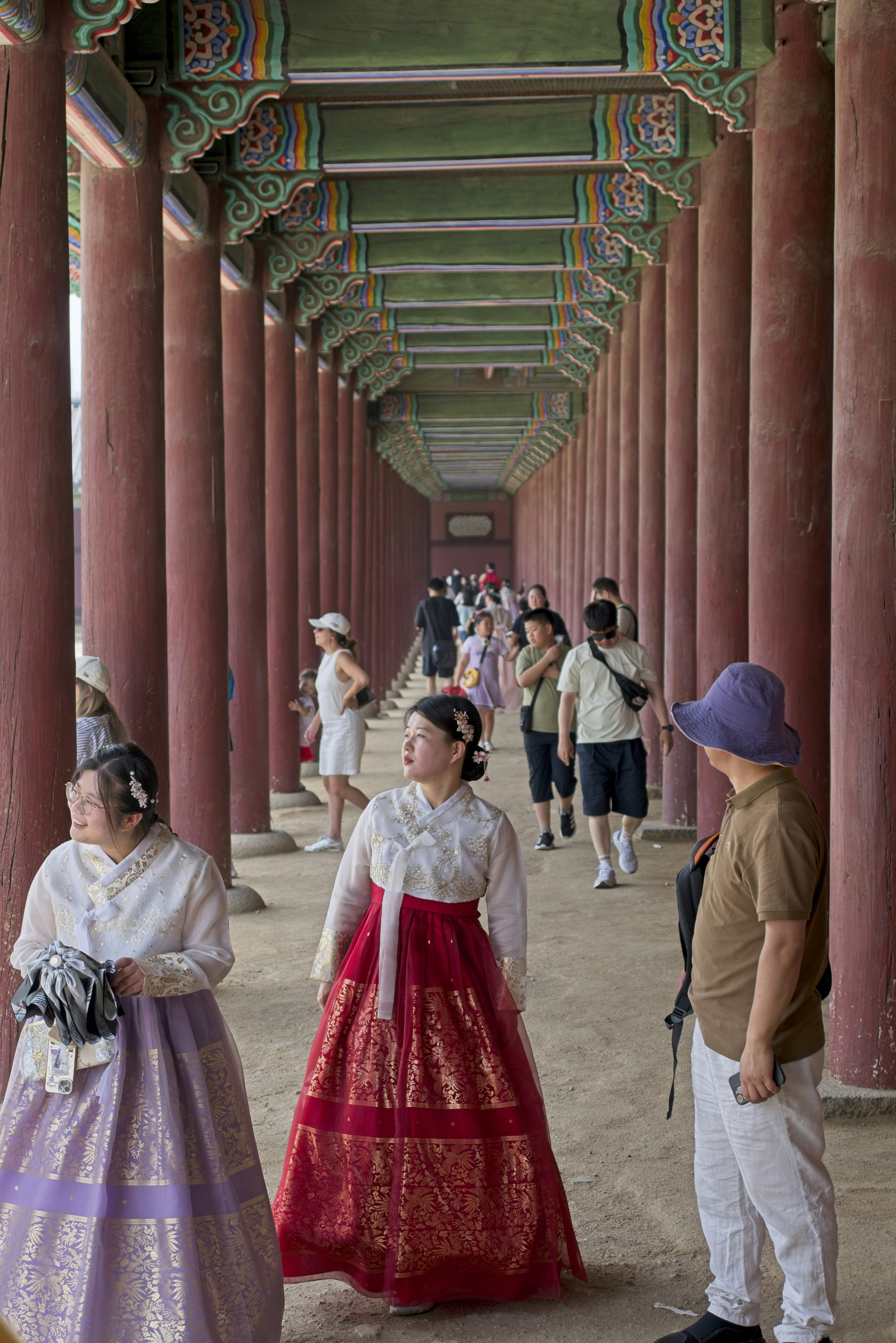 Red-Hued Kimono Corridor: Travelers Amid Pale Timber and Painted Beams