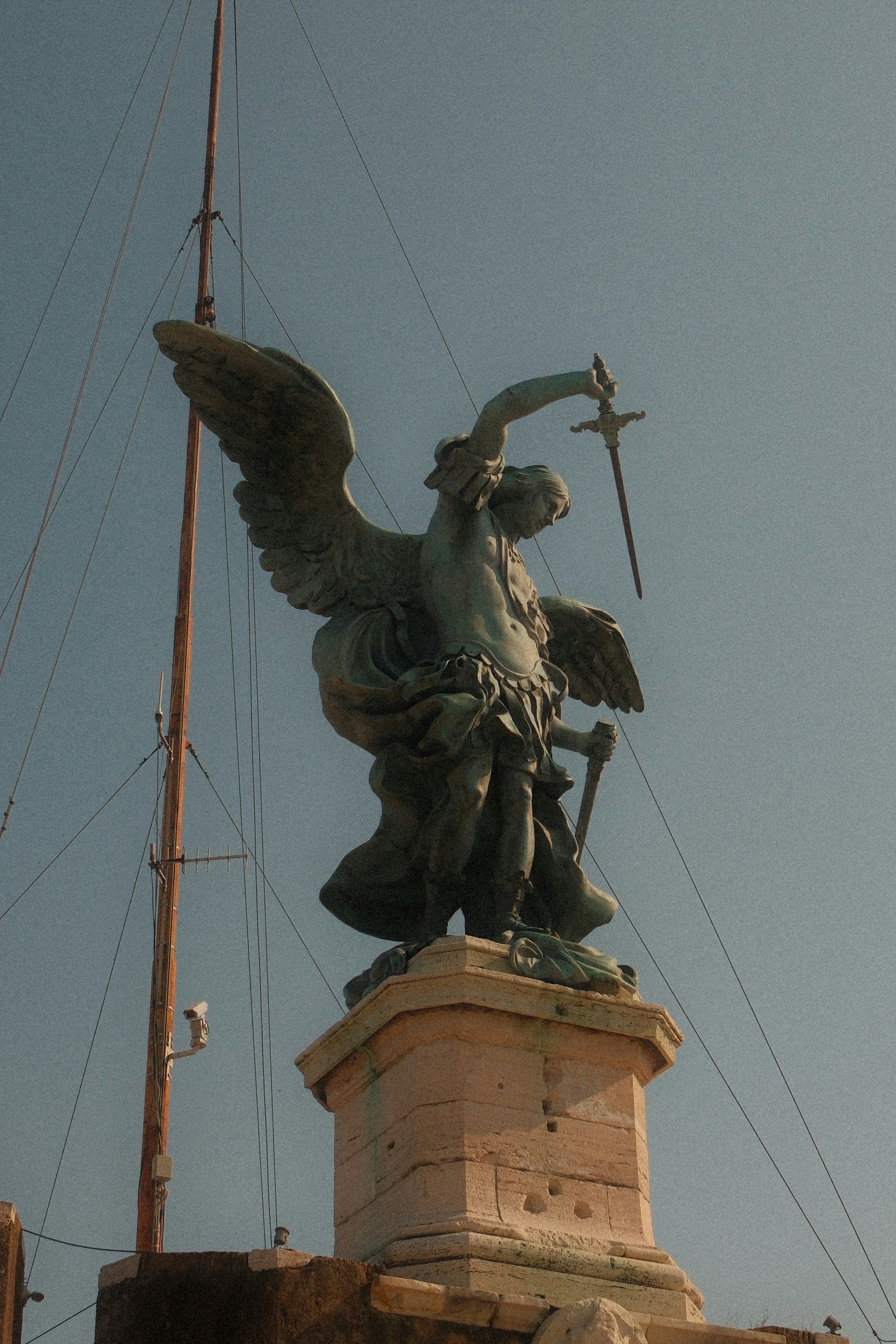 Winged Sentinel: A Bronze Angel Holds a Dagger aloft Against a Sailor's Mast