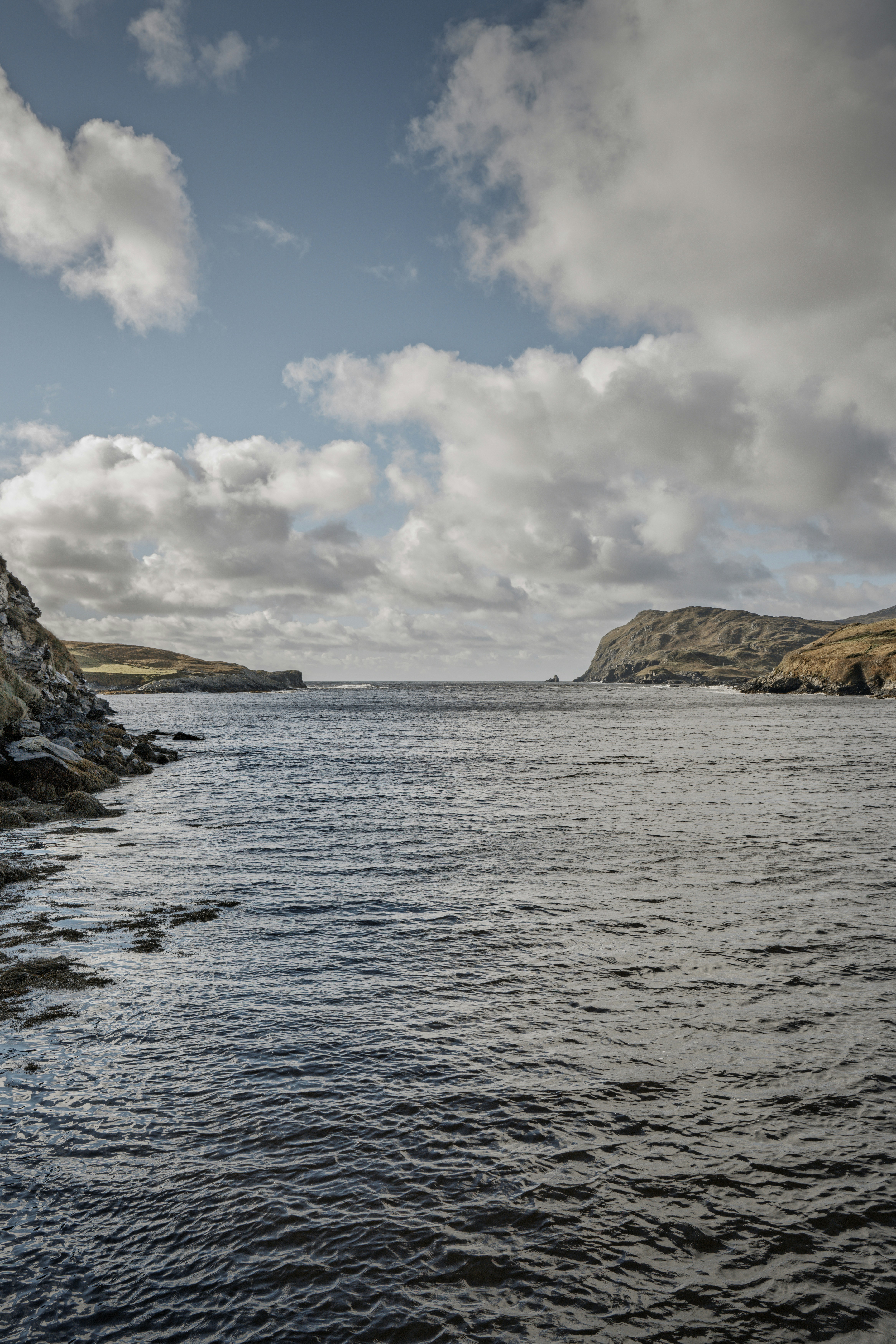 Coastal scene of calm sea between rocky shoreline cliffs and distant headlands under a partly cloudy sky; no people or vehicles, natural landscape capturing vast horizon. This is a landscape photograph.