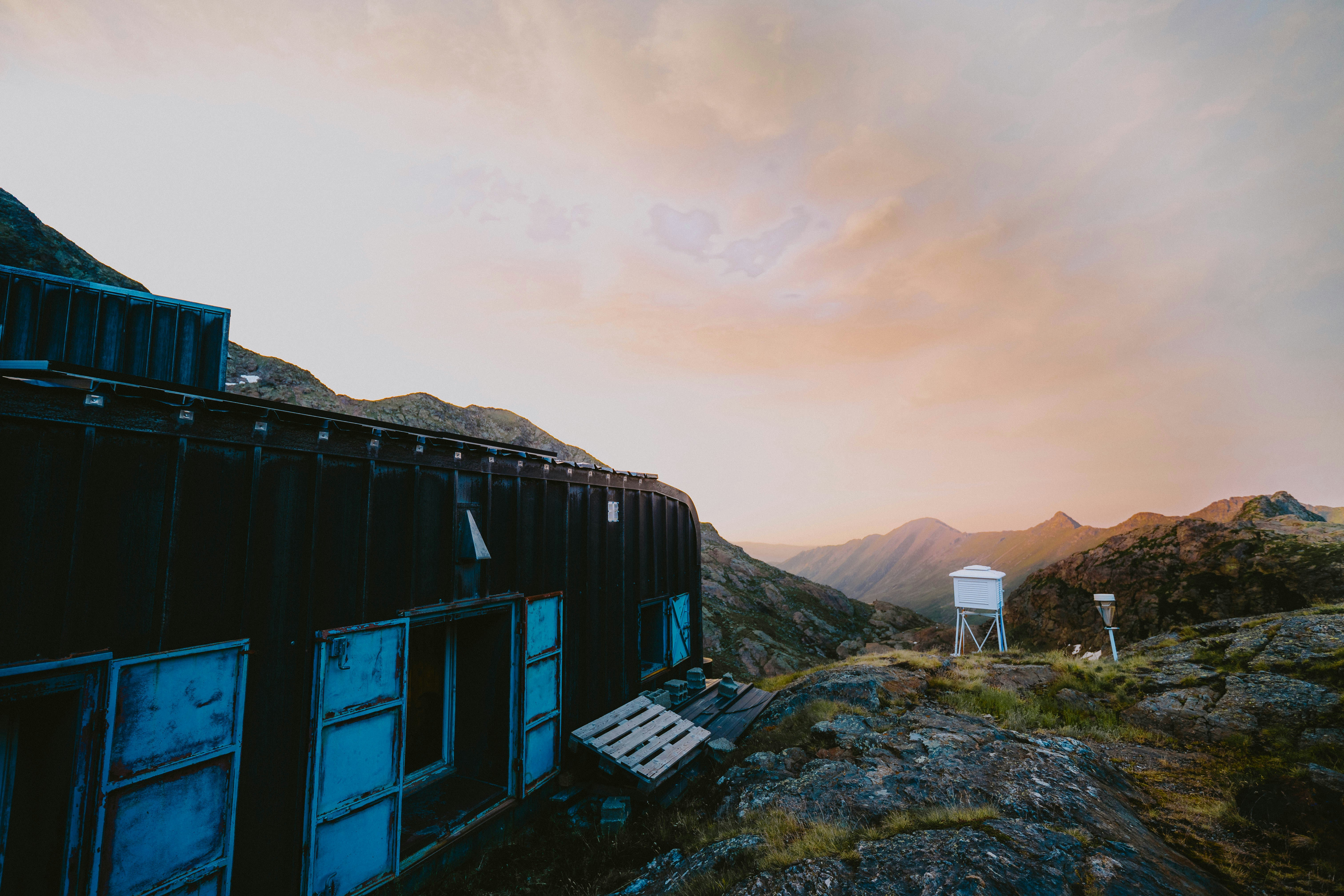 Weathered coastal outpost sits against rocky terrain with a soft sunset glow over distant peaks.