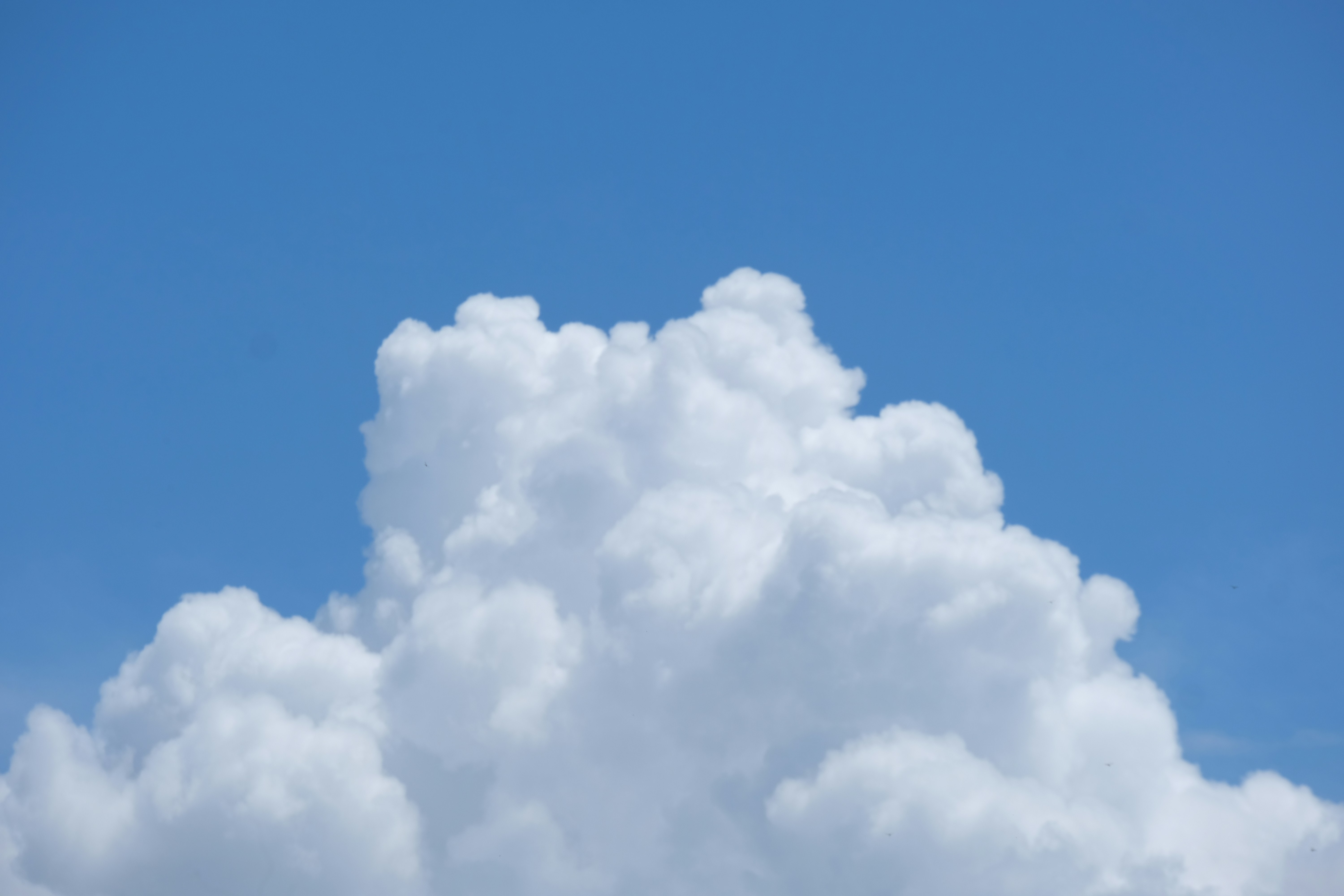 A towering cumulus formation rises over a vivid blue sky, occupying the upper portion of the frame. The image emphasizes the cloud mass and airiness, suitable for illustrating weather or atmospheric calm. Logo-free sky texture.