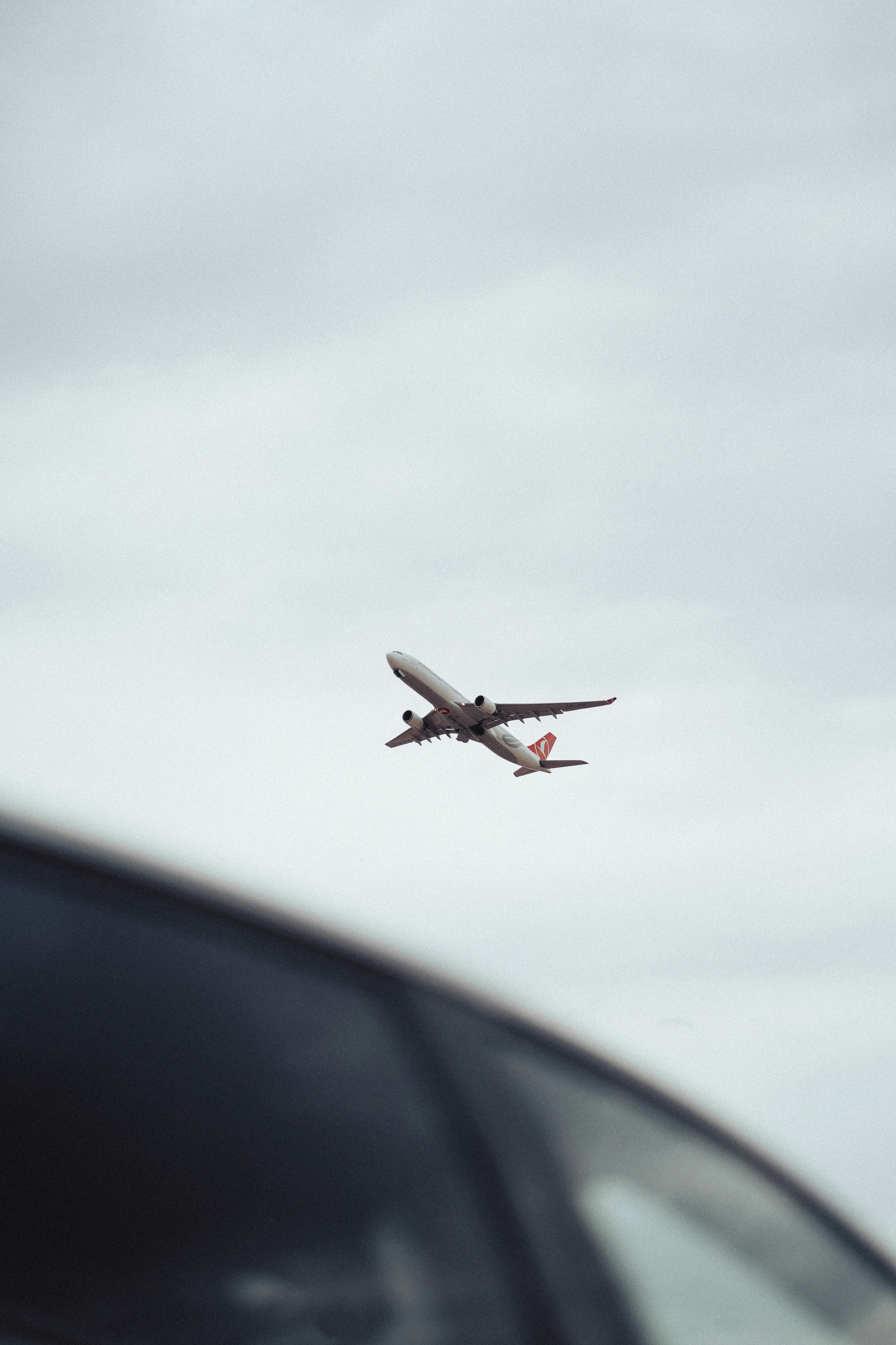 Airliner in ascent: a distant jet framed by car hood silhouettes