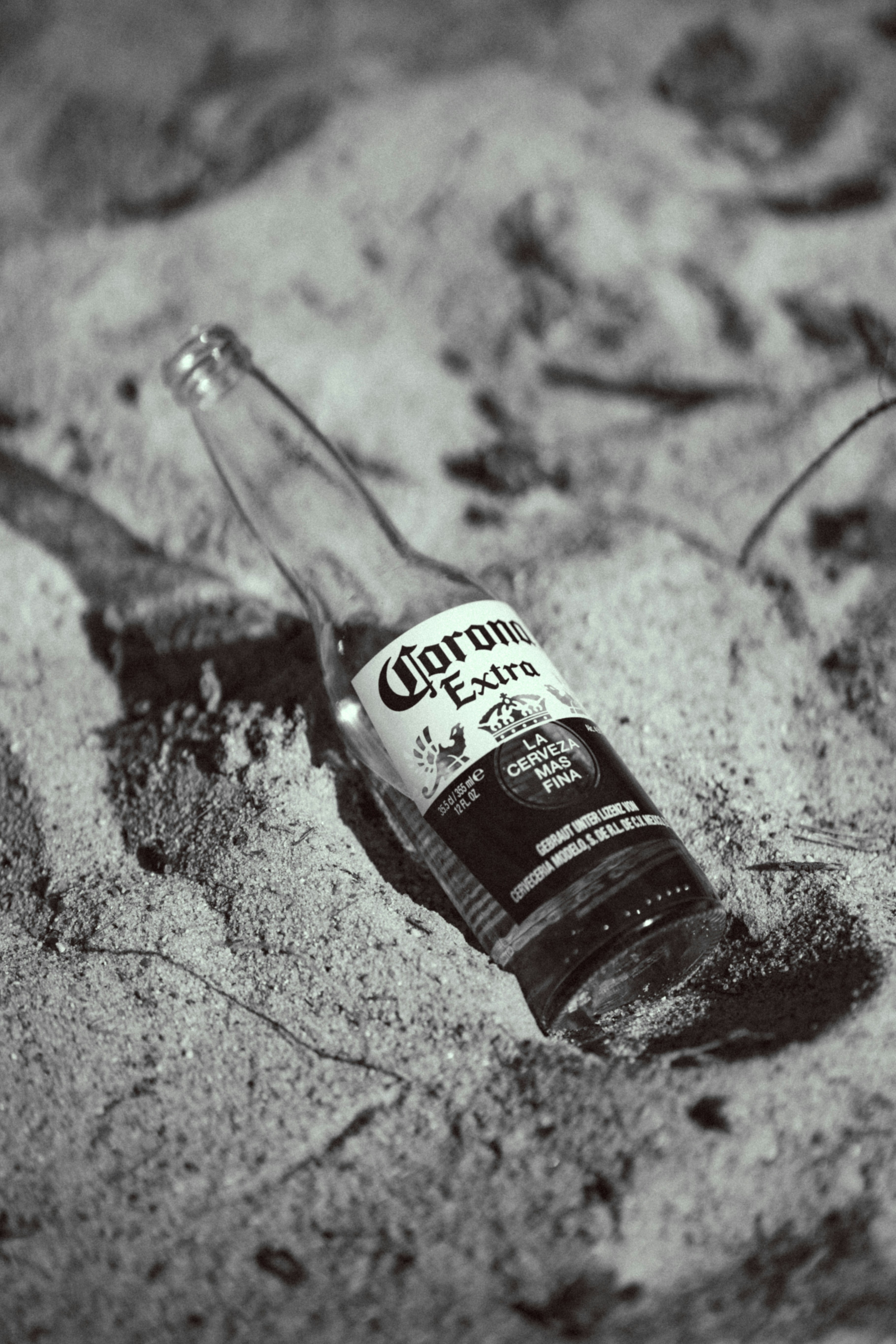 A black and white empty corona extra bottle on sand.
