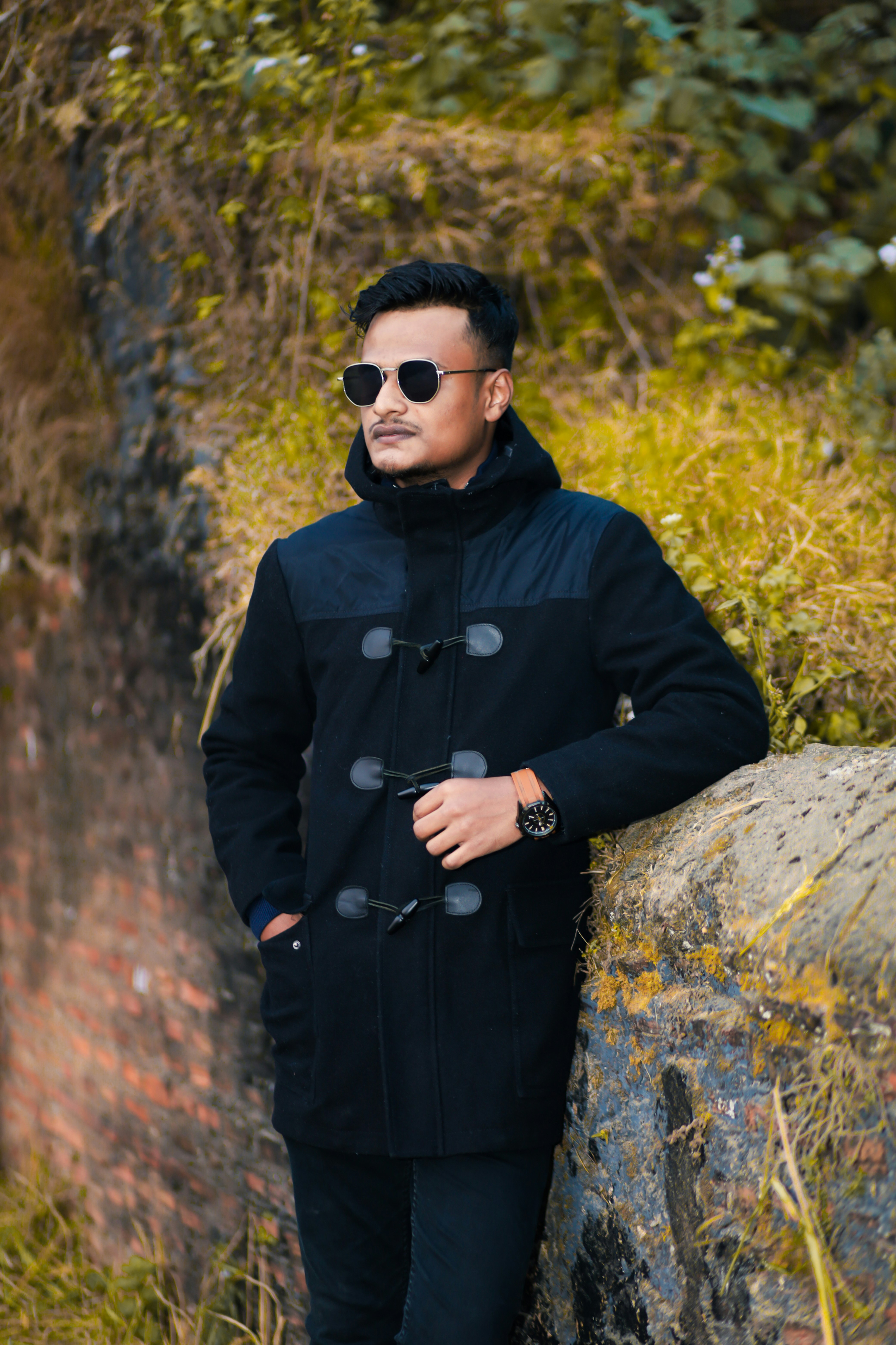 Coated in shadow and steel: a man leans against mossy stone in dusk-lit outdoors