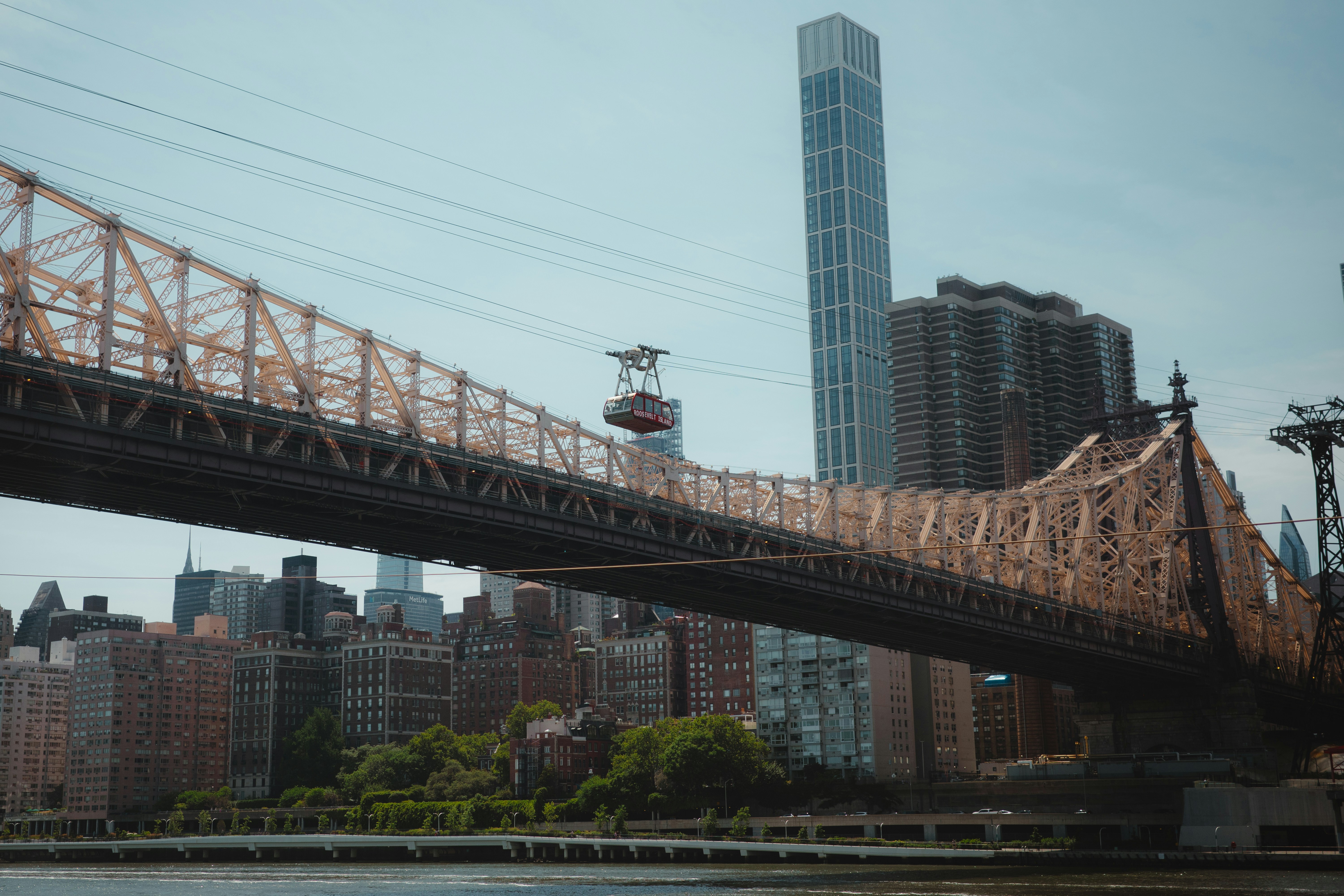 Sunlit bridge spans the river with skyline high-rises and a cable car visible, forming a dynamic urban landscape.
