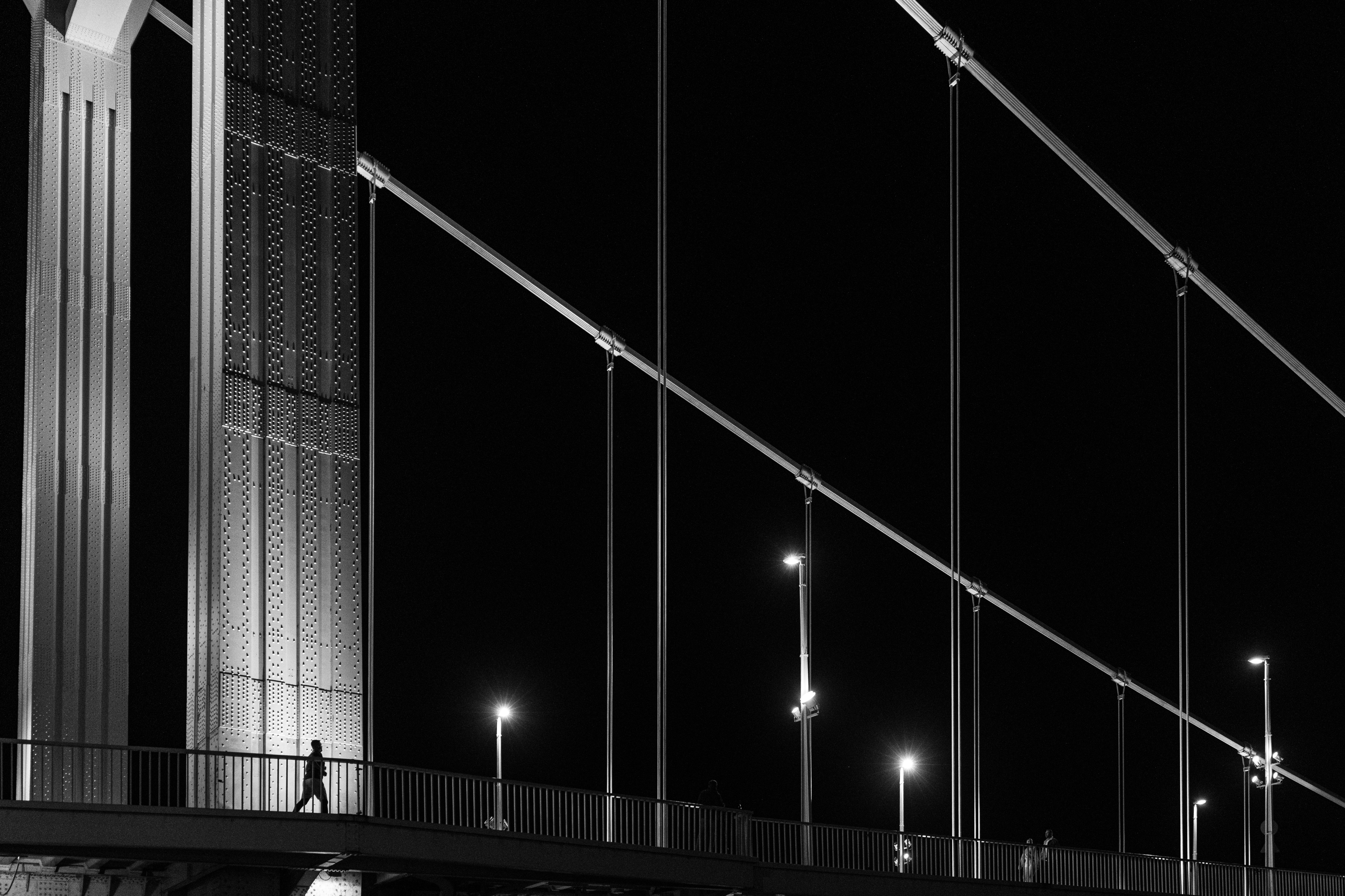 Midnight Suspension: A lone pedestrian on a lit bridge