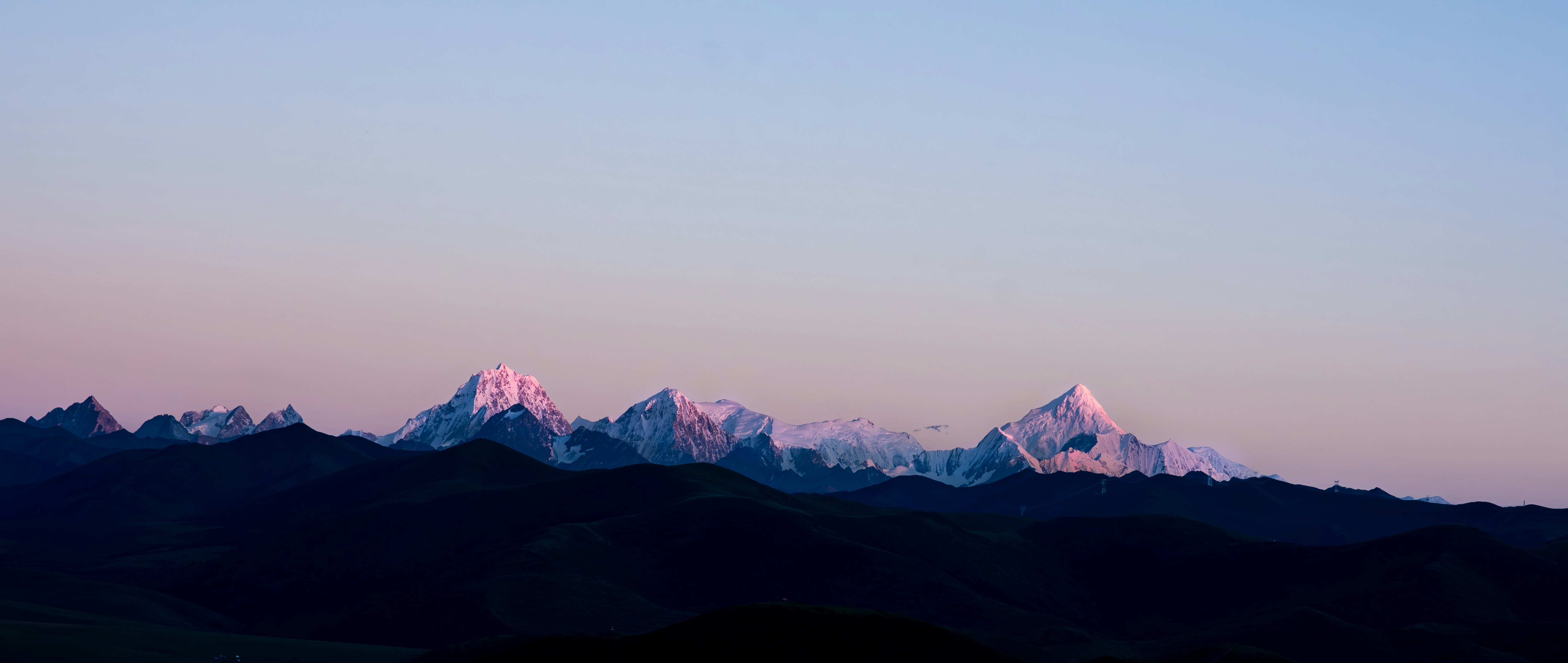 Snow-capped peaks lit by dawn glow over a quiet valley