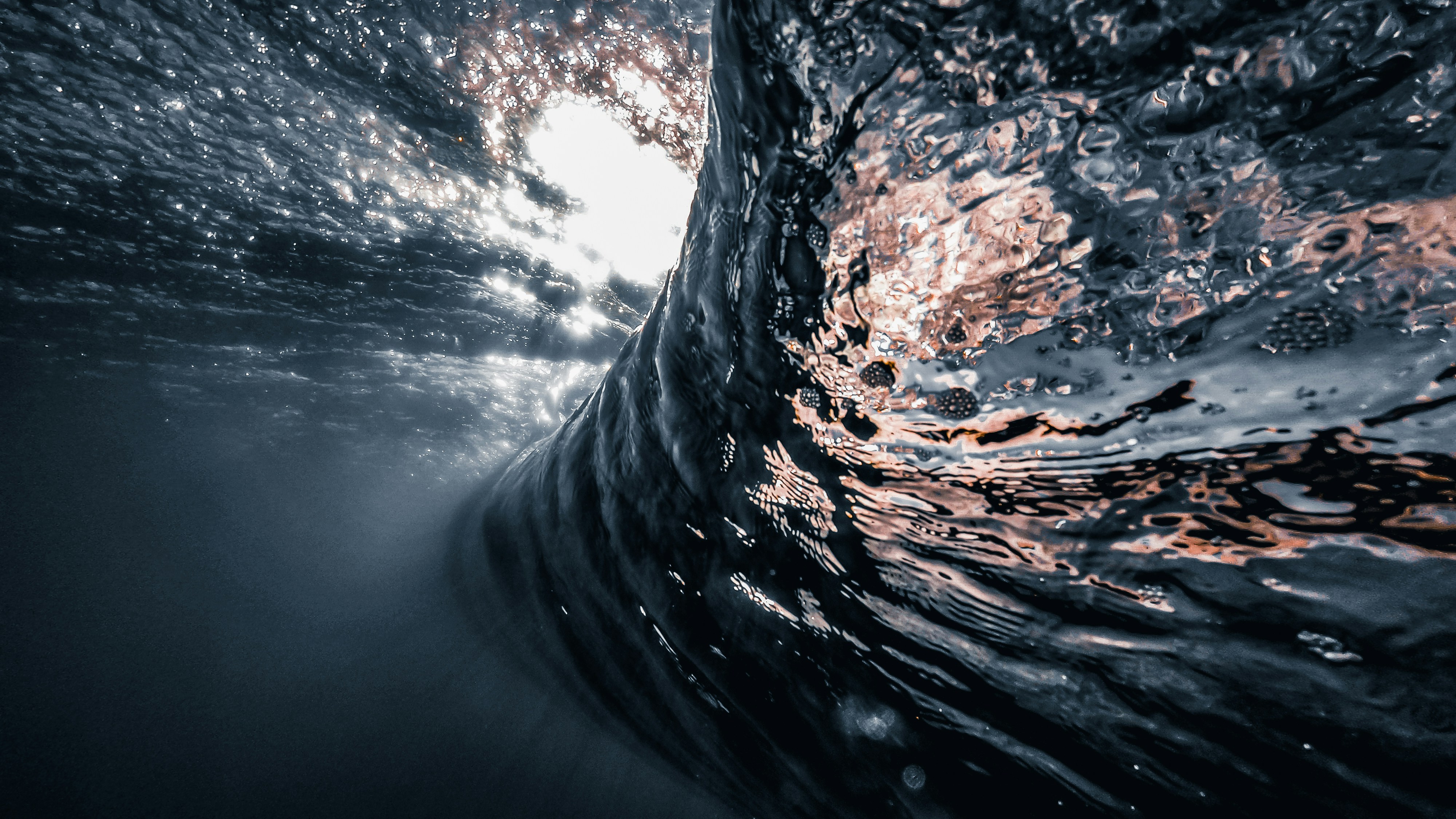 High-contrast underwater barrel wave with sunlit surface peering through, creating a dramatic tunnel of water and reflections.