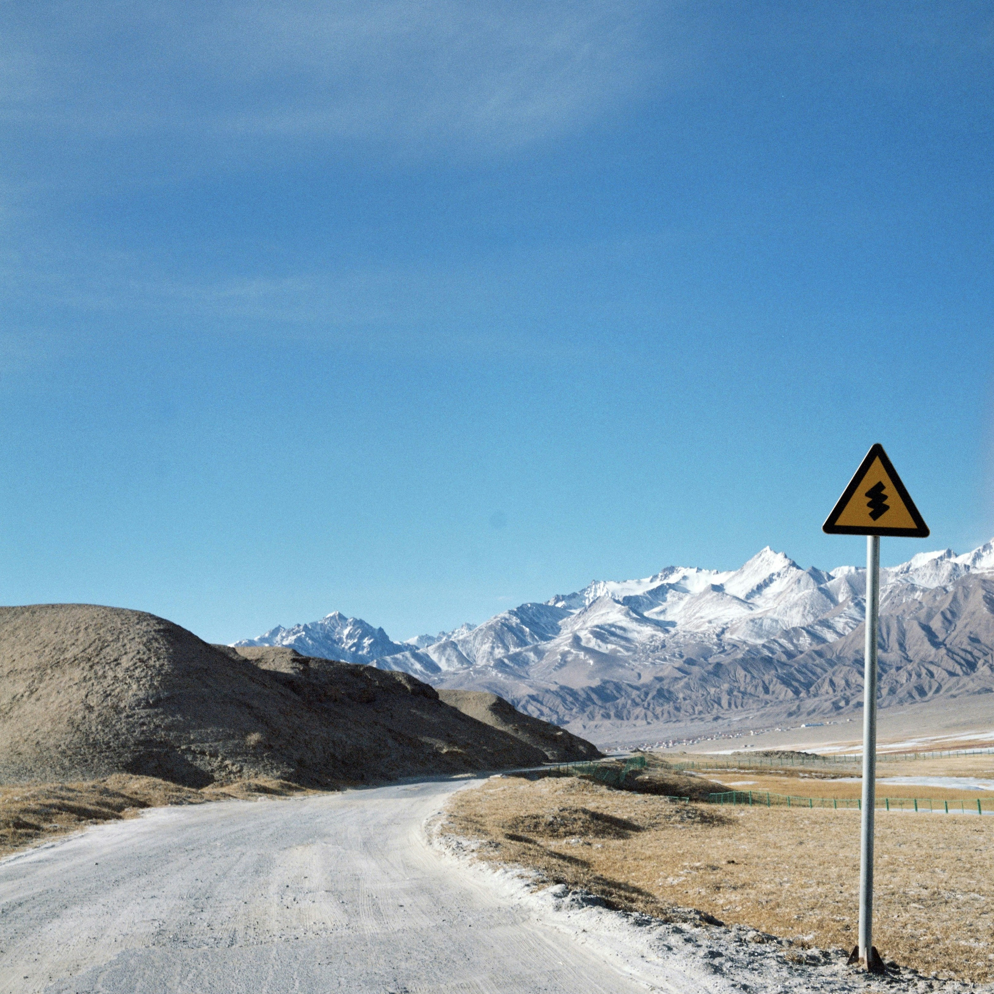 Desert Road Toward Snow-Capped Peaks Under a Clear Blue Sky