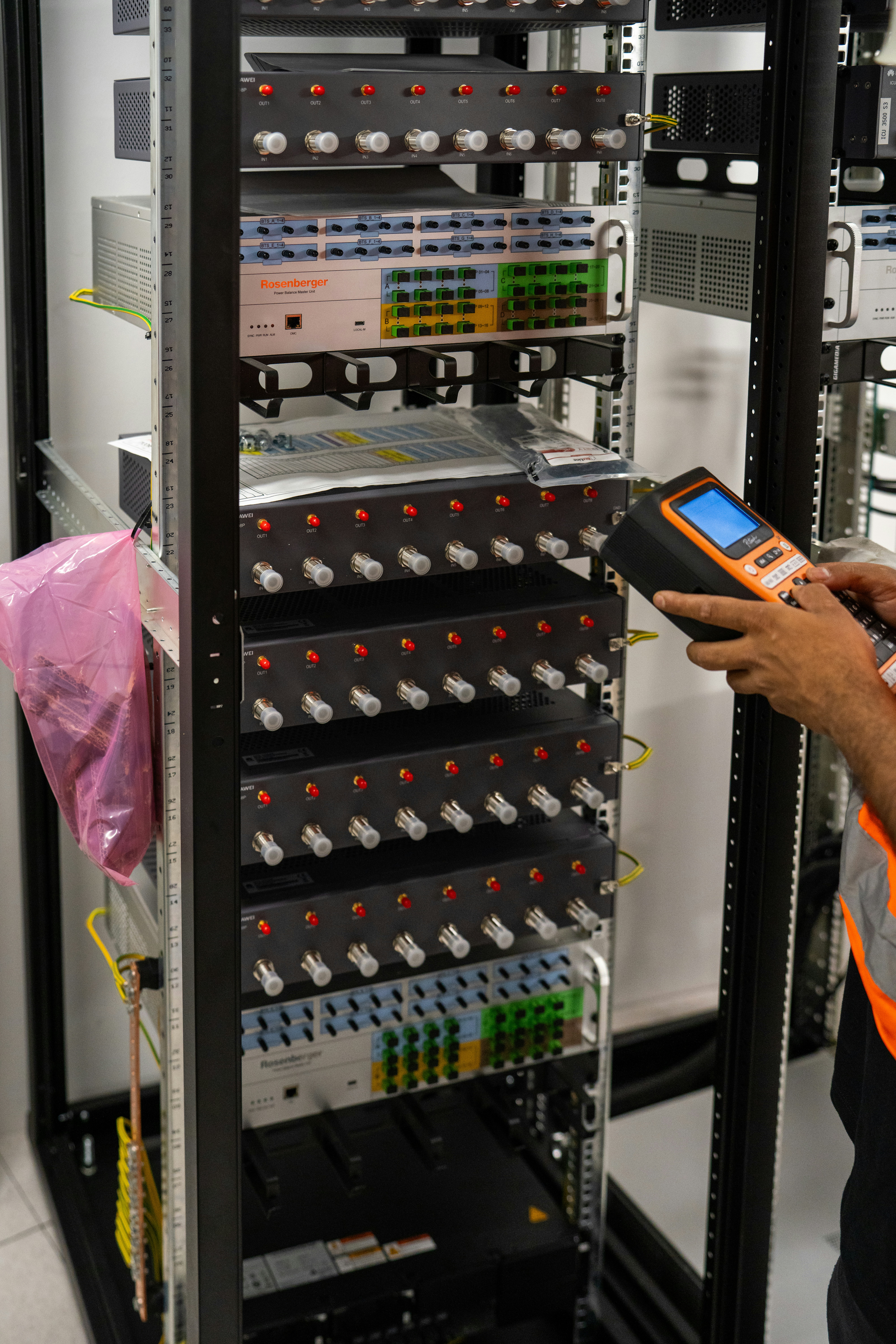 A technician uses a handheld device to probe a rack-mounted network switch/patch panels in a server cabinet, with cables and status LEDs visible.