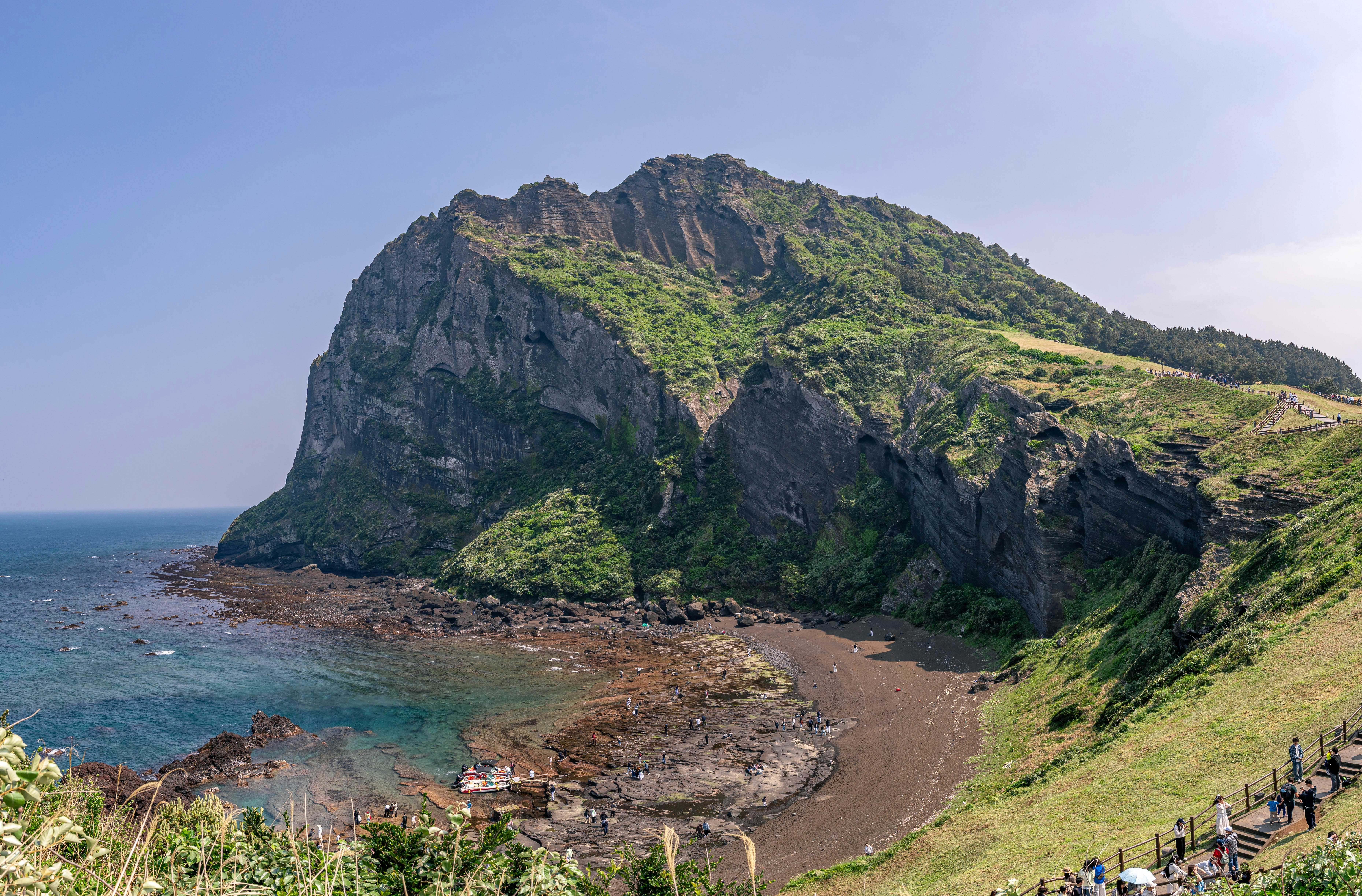 Rocky coastal promontory with green slopes and a small beach cove along a blue sea.
