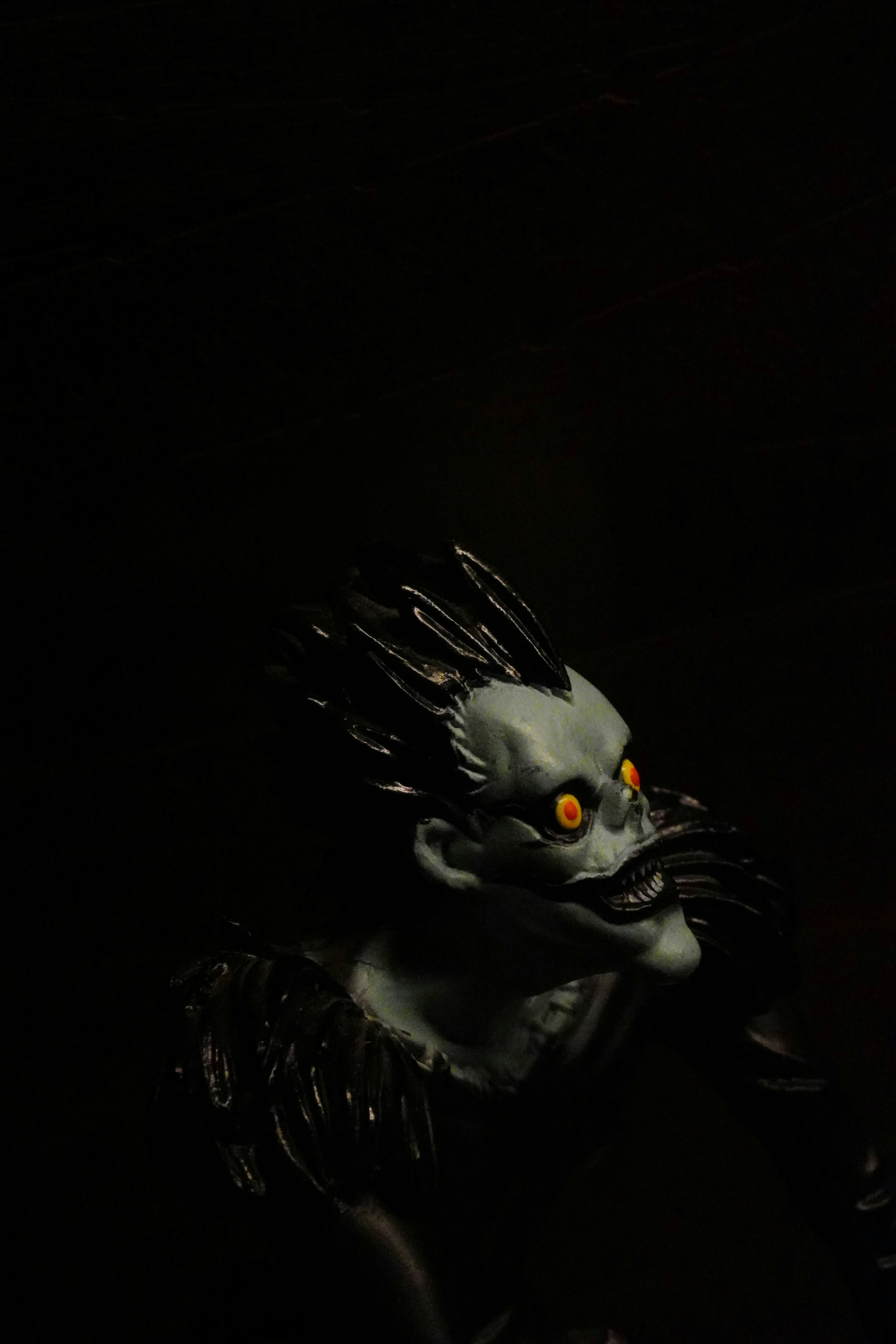Dark, moody portrait of a pale creature with glowing orange eyes under minimal light, emphasizing its sinister features.