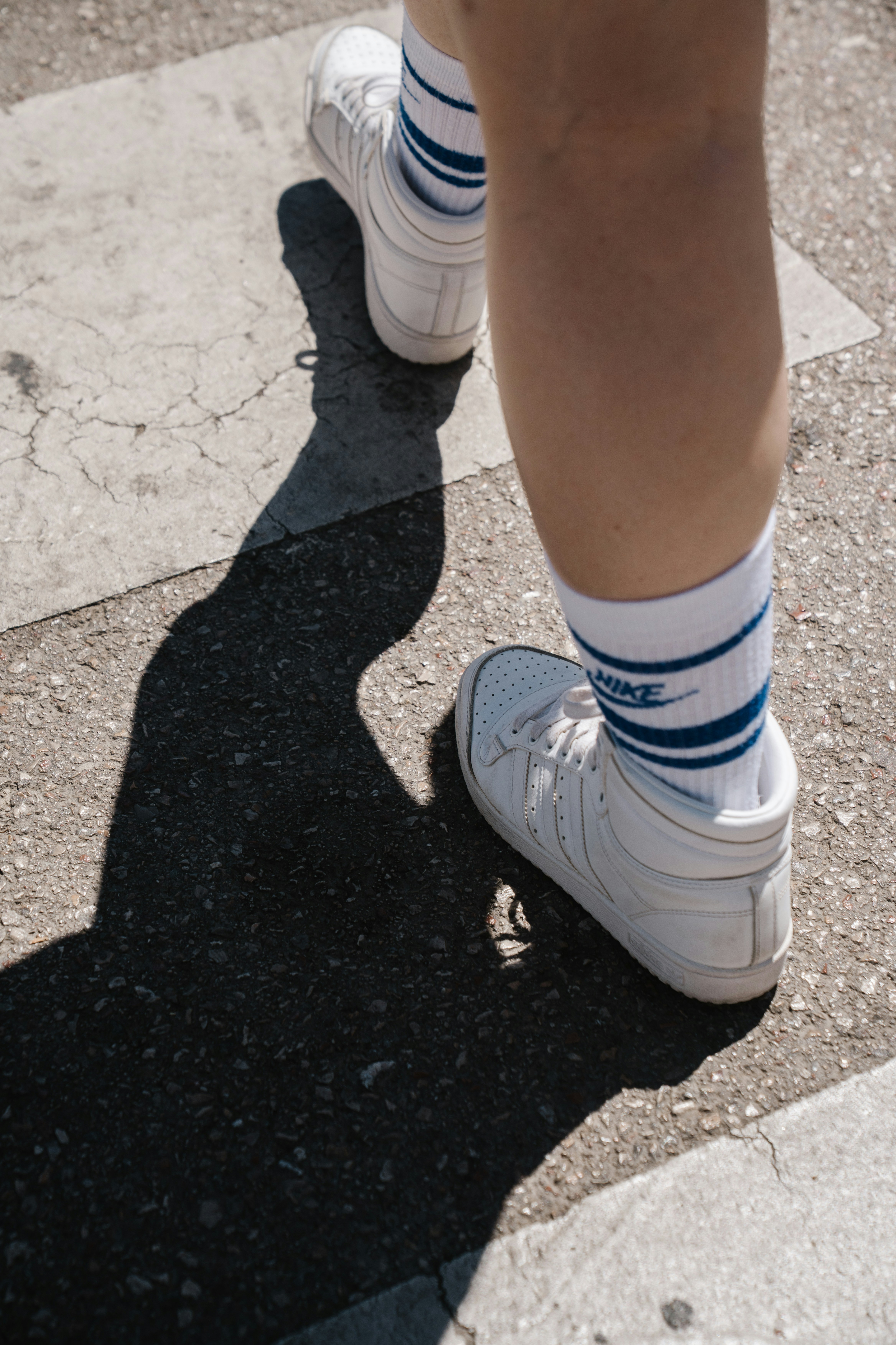 Stride and Shadow: White sneakers on a sunlit pavement