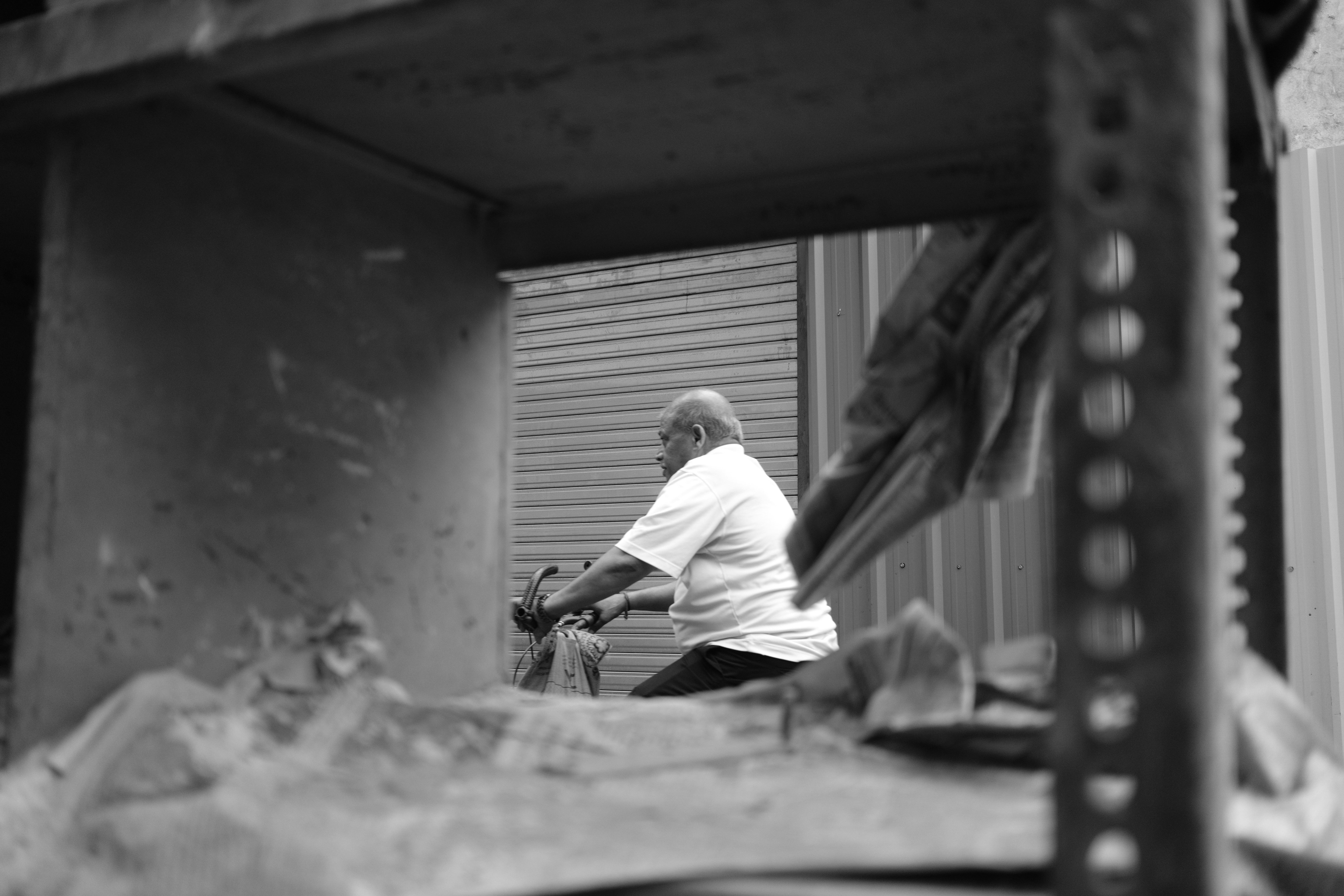 Person operating a bicycle amid urban debris framed by industrial rigging