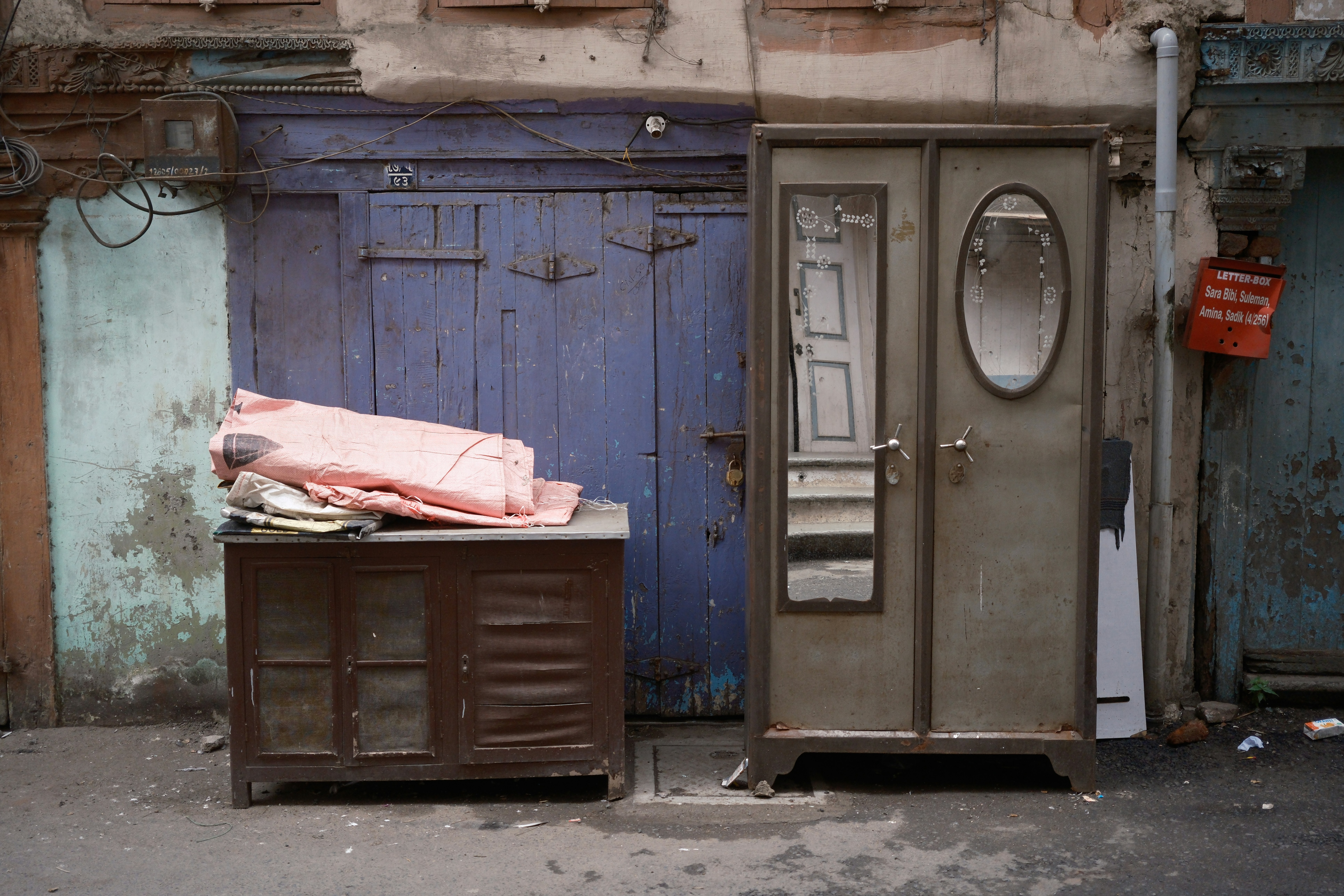 A Quiet Streetfront: A Cabinet, a Mirror, and a Pink-Tinted Sack