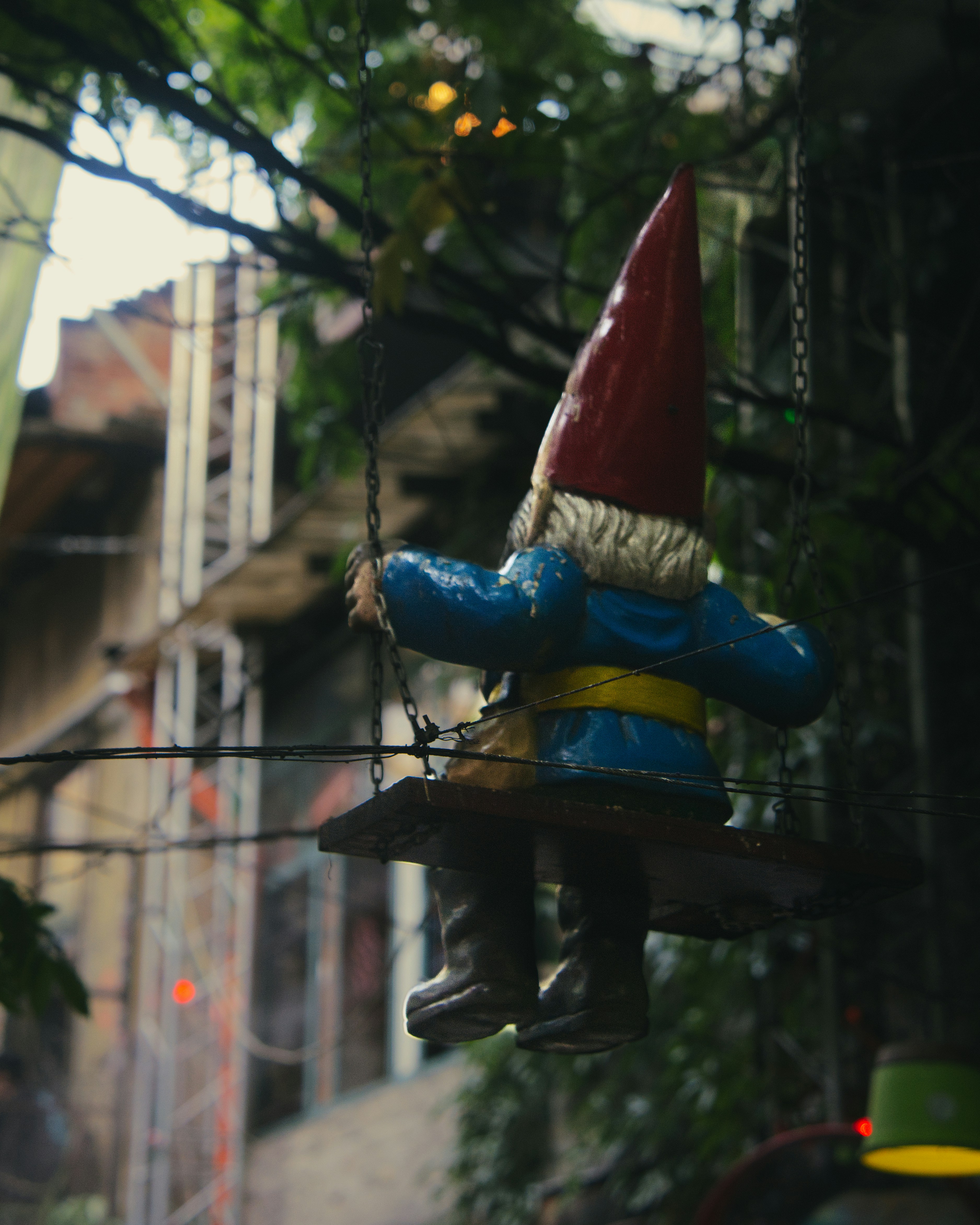 Swinging Gnome: A Weathered Playground Guardian Under Tree Canopy