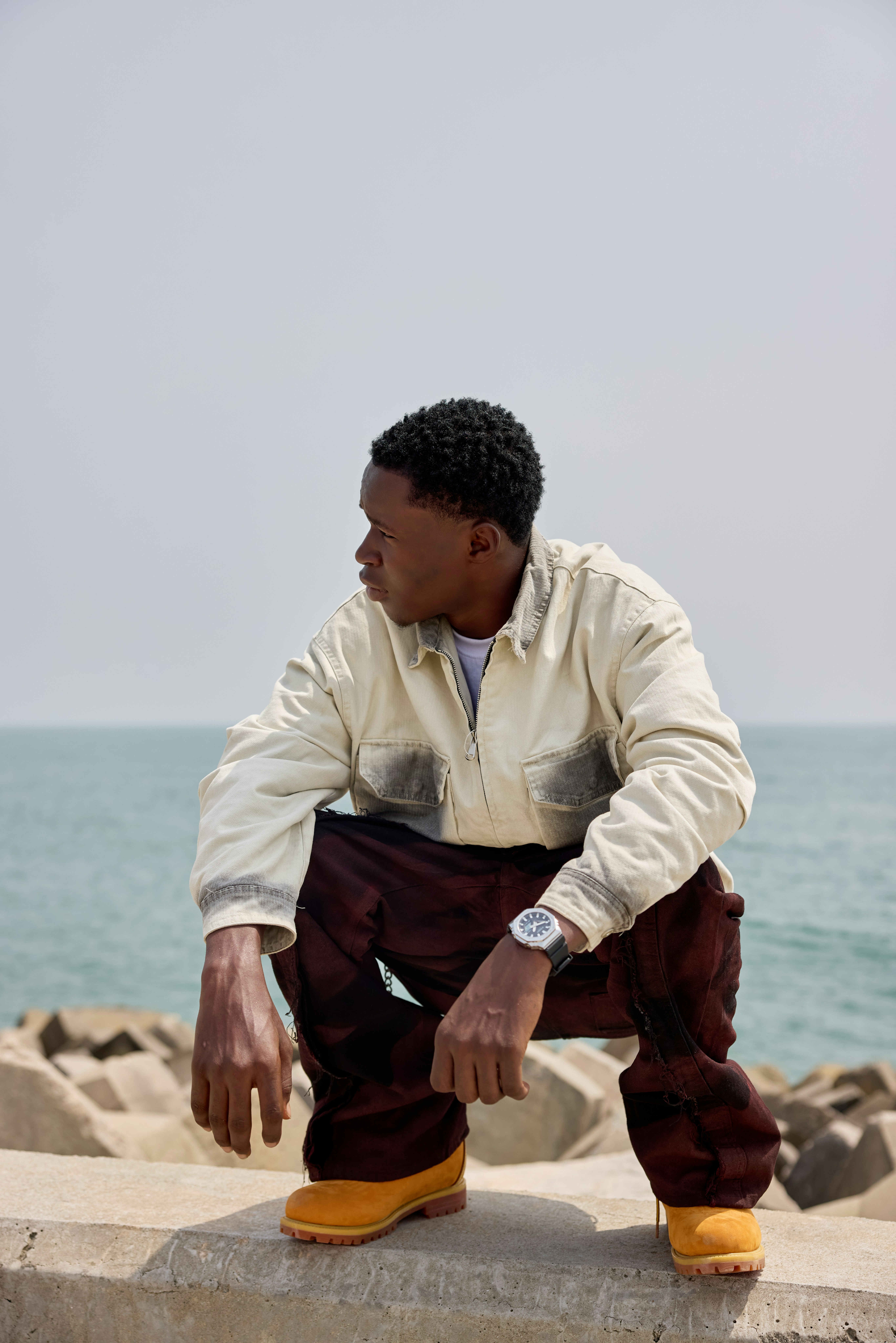Coiled stillness: a man crouches by the shoreline with a calm gaze