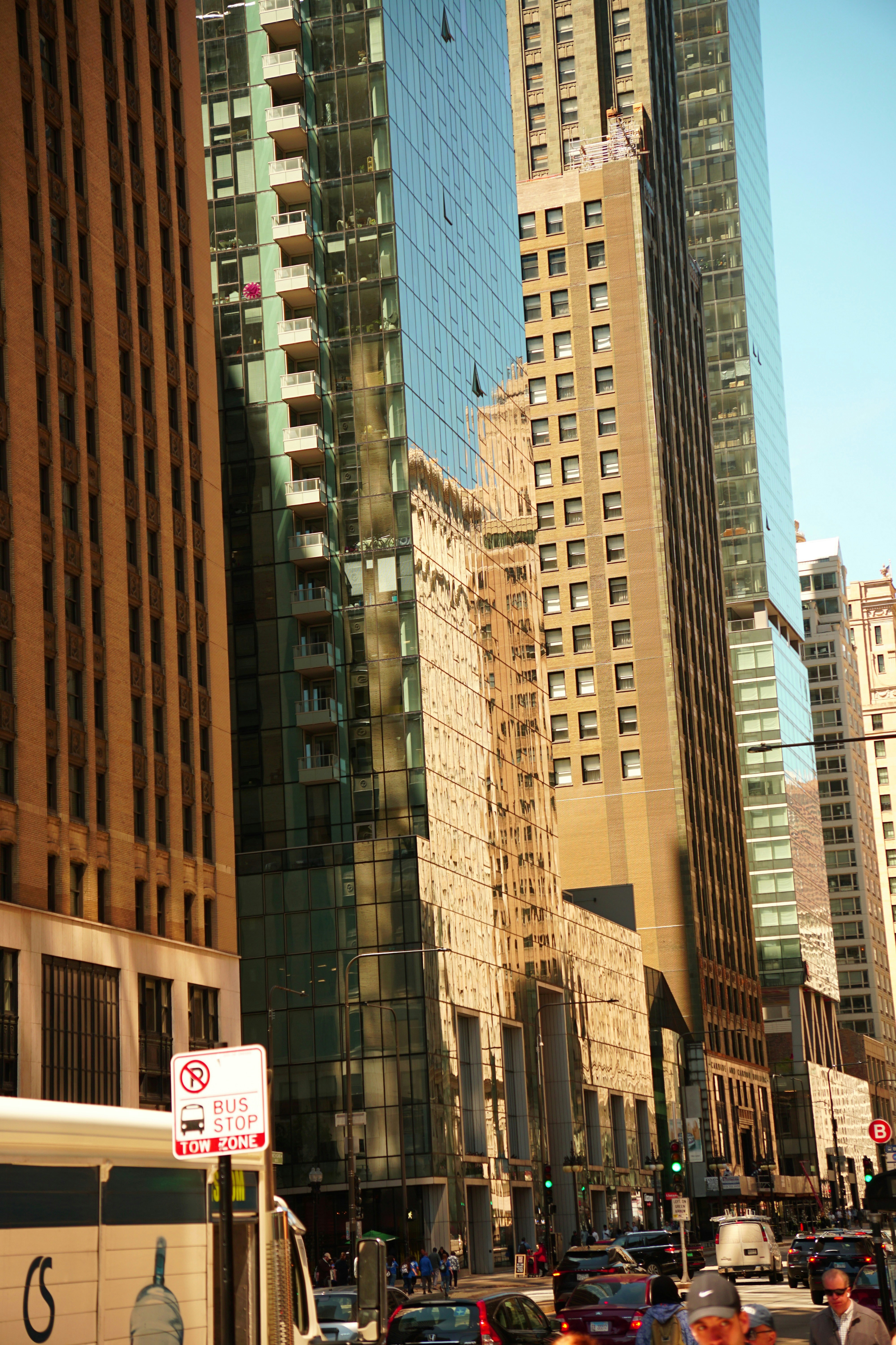 Skyscrapers form a corrugated canyon with reflective glass facades catching the afternoon light; a busy street below shows vehicles and pedestrians framed by towering glass towers.