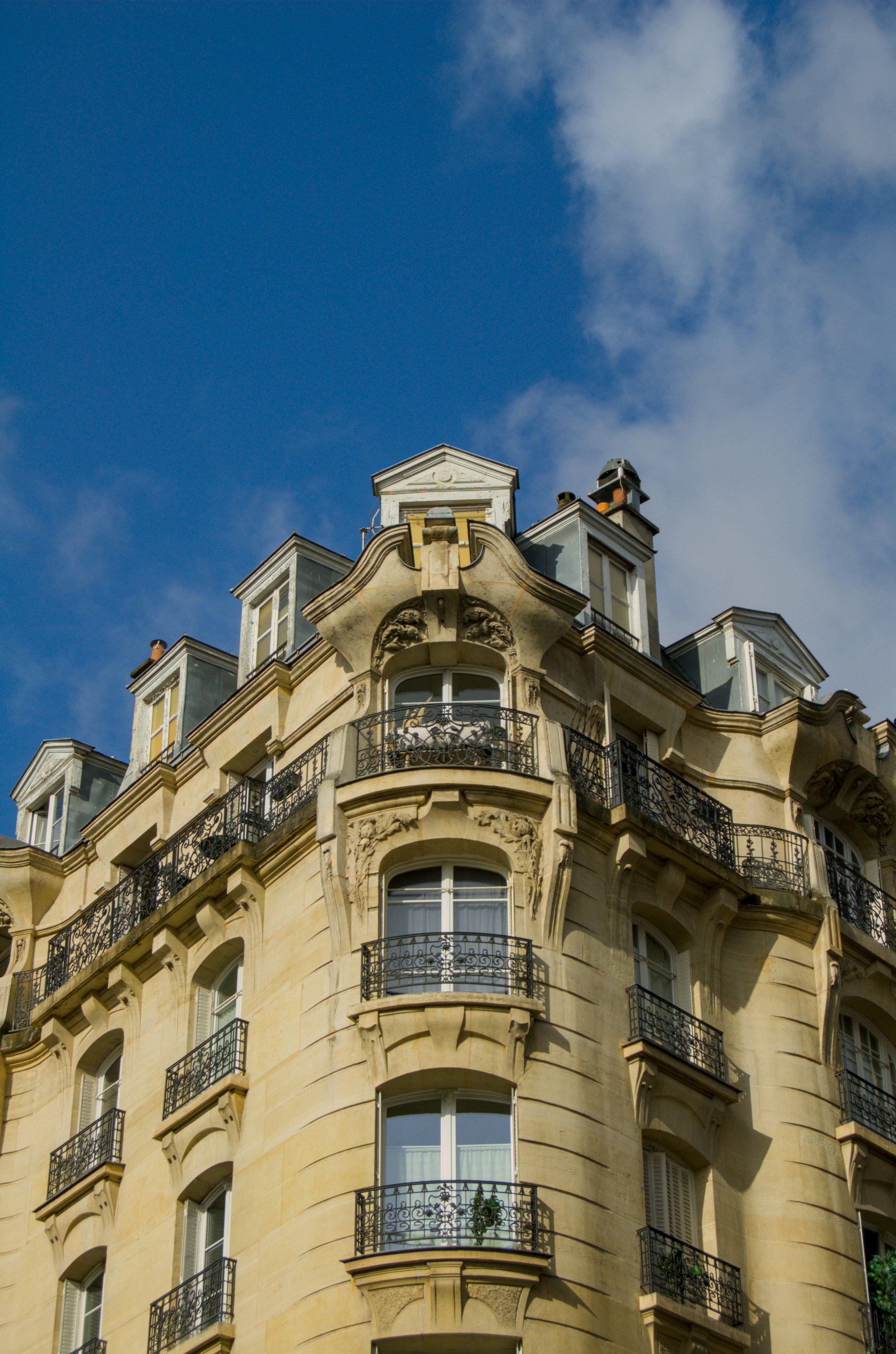 Sunlit Parisian Facade: Curved Balconies and Ornate Stonework Rising to the Sky