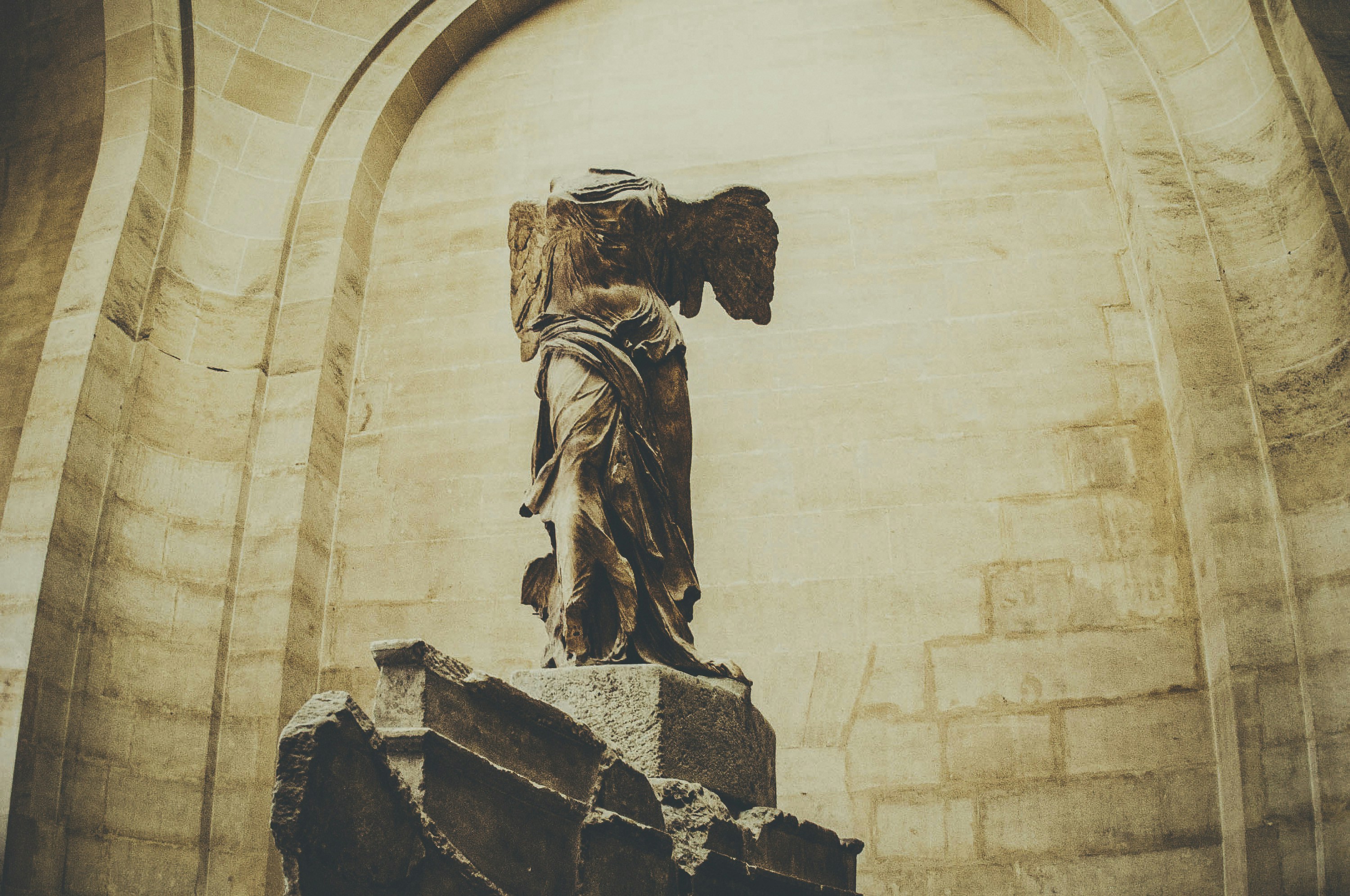Vitória de Samotrácia - View ( 2013 ) A dramatic angled photograph of the Winged Victory of Samothrace (Vitória de Samotrácia), showcasing its marble wings, flowing drapery, and imposing stance from a powerful perspective that emphasizes its dynamic movement and ancient Greek sculptural genius.