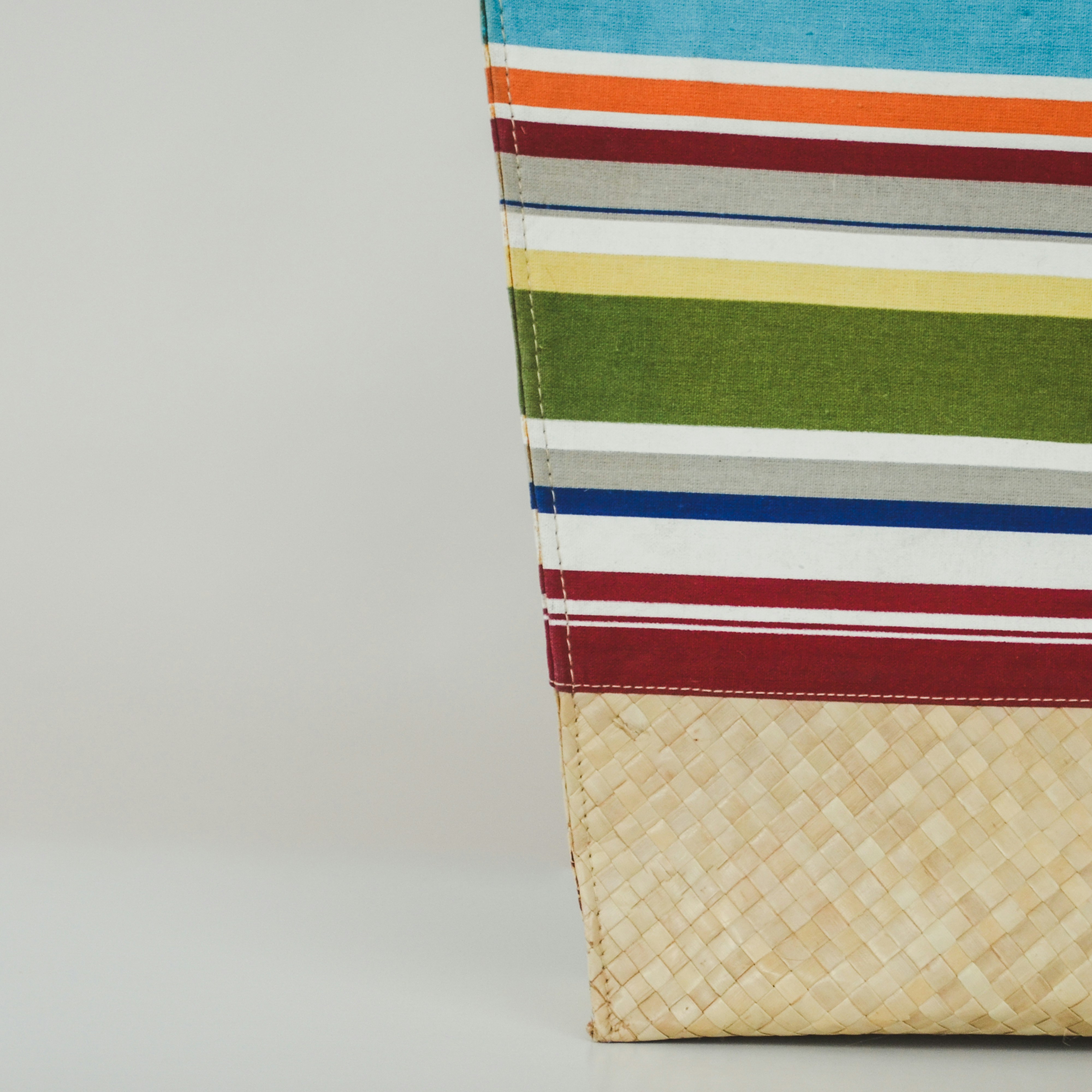 Color Stripes and woven texture: a sunlit shopping tote at the edge of a pale backdrop