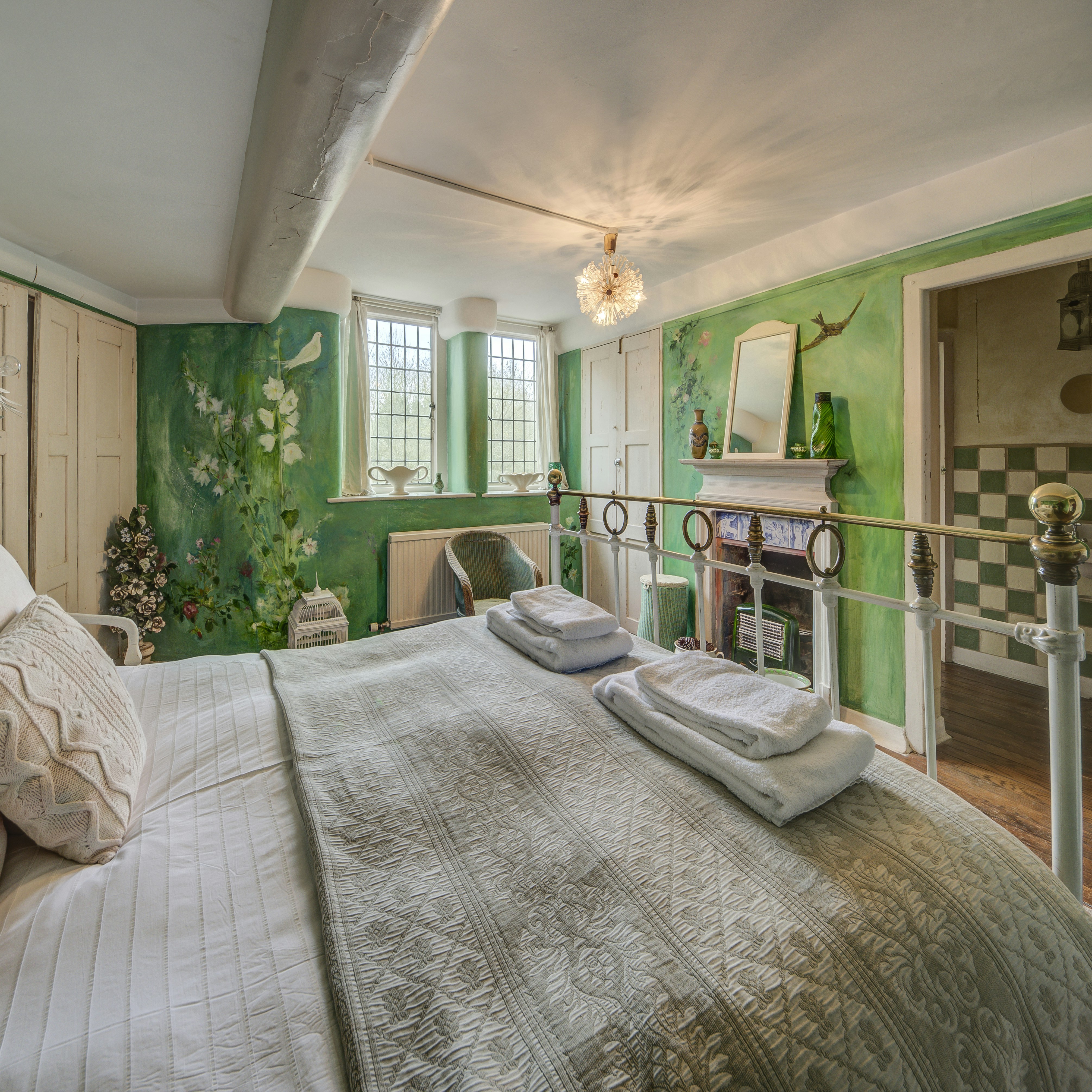 Lush green walls enclose a sunlit bedroom with a tall bed and vintage accents, creating a tranquil retreat.