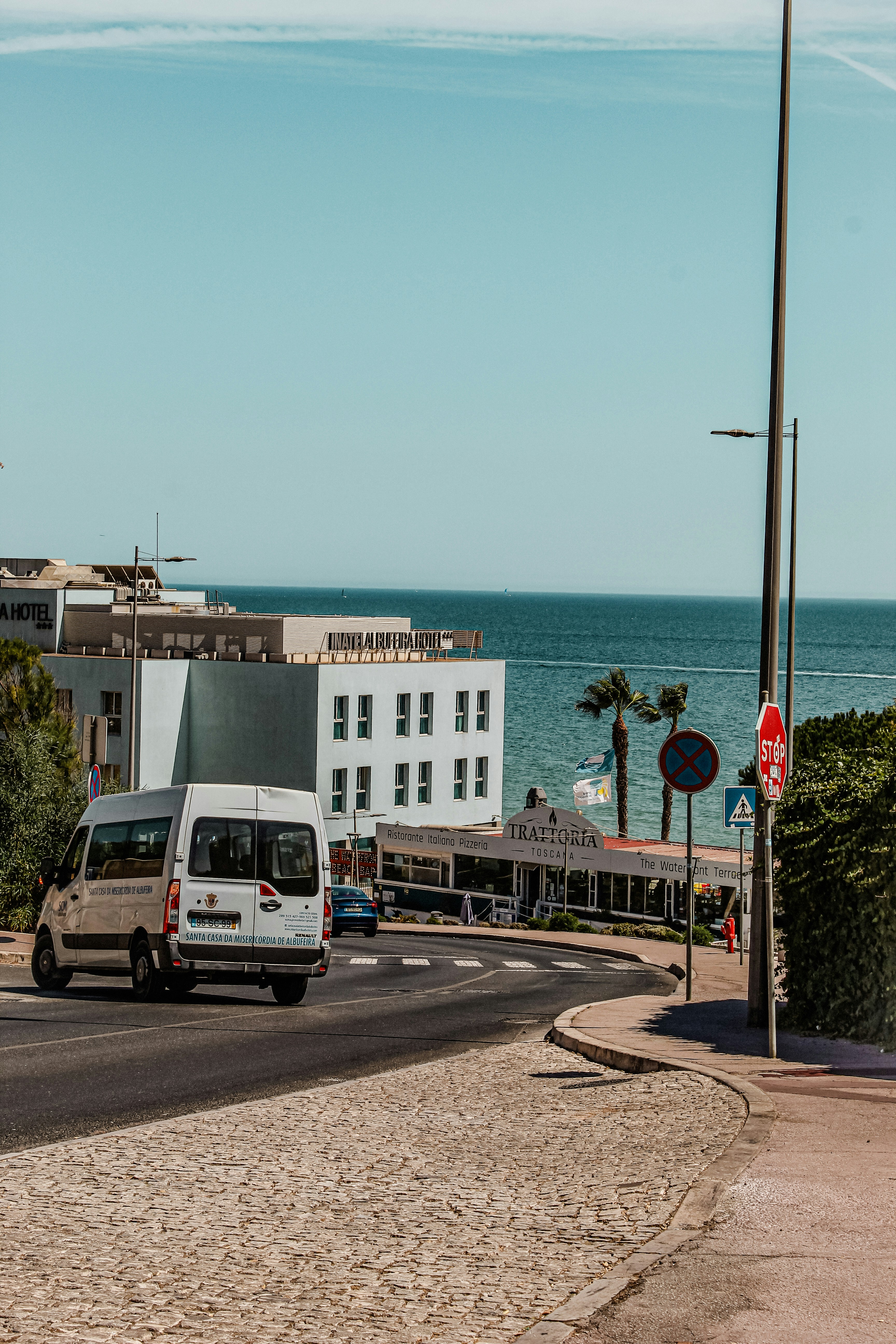 White van driving on a coastal road overlooking the ocean.