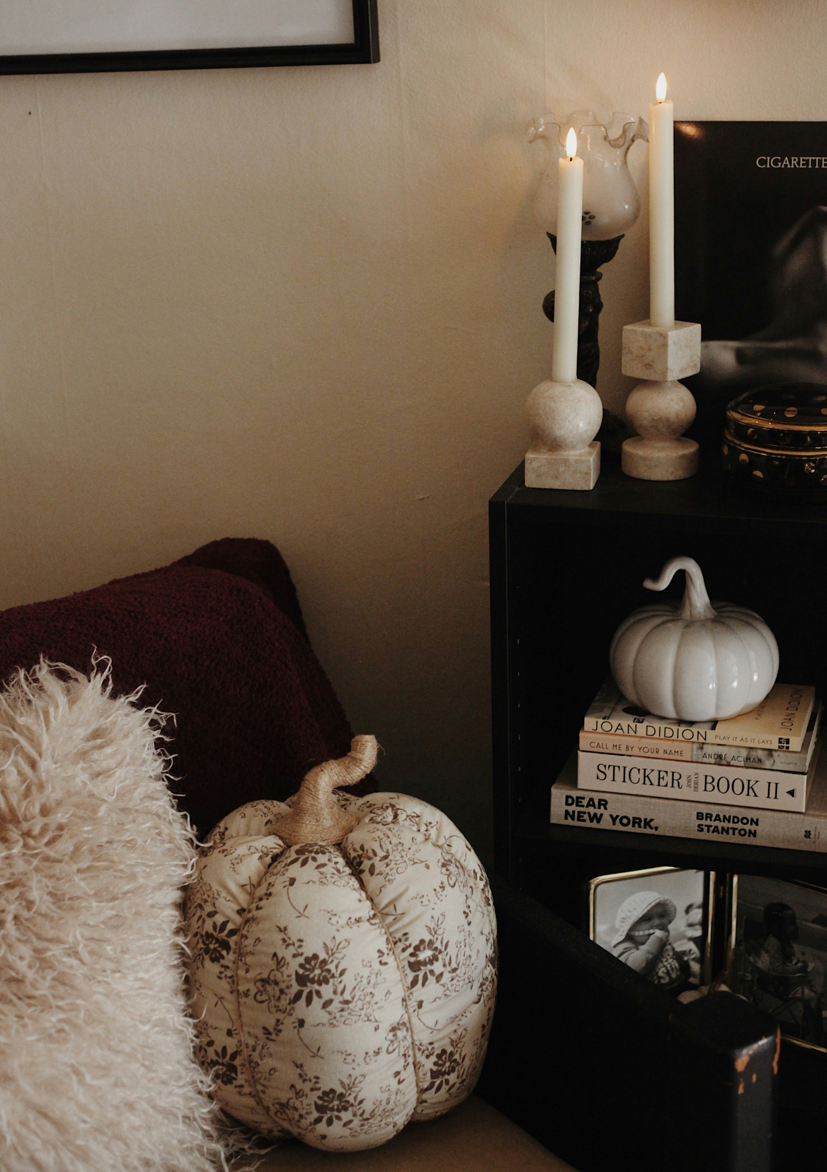 Candles, pumpkins, and books: a cozy autumn vignette on a black shelf