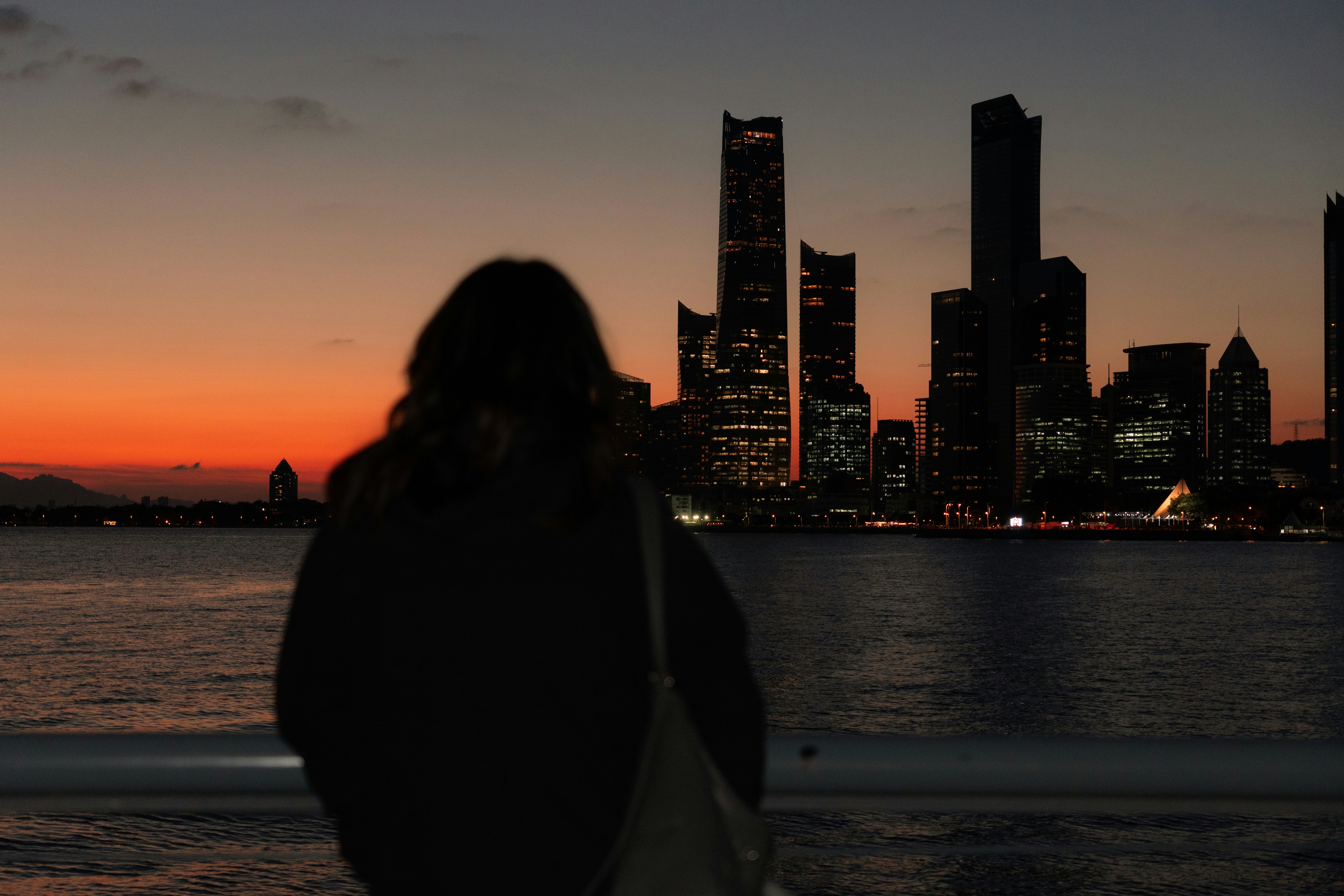 Evening silhouettes: watcher at the water’s edge with a city silhouette