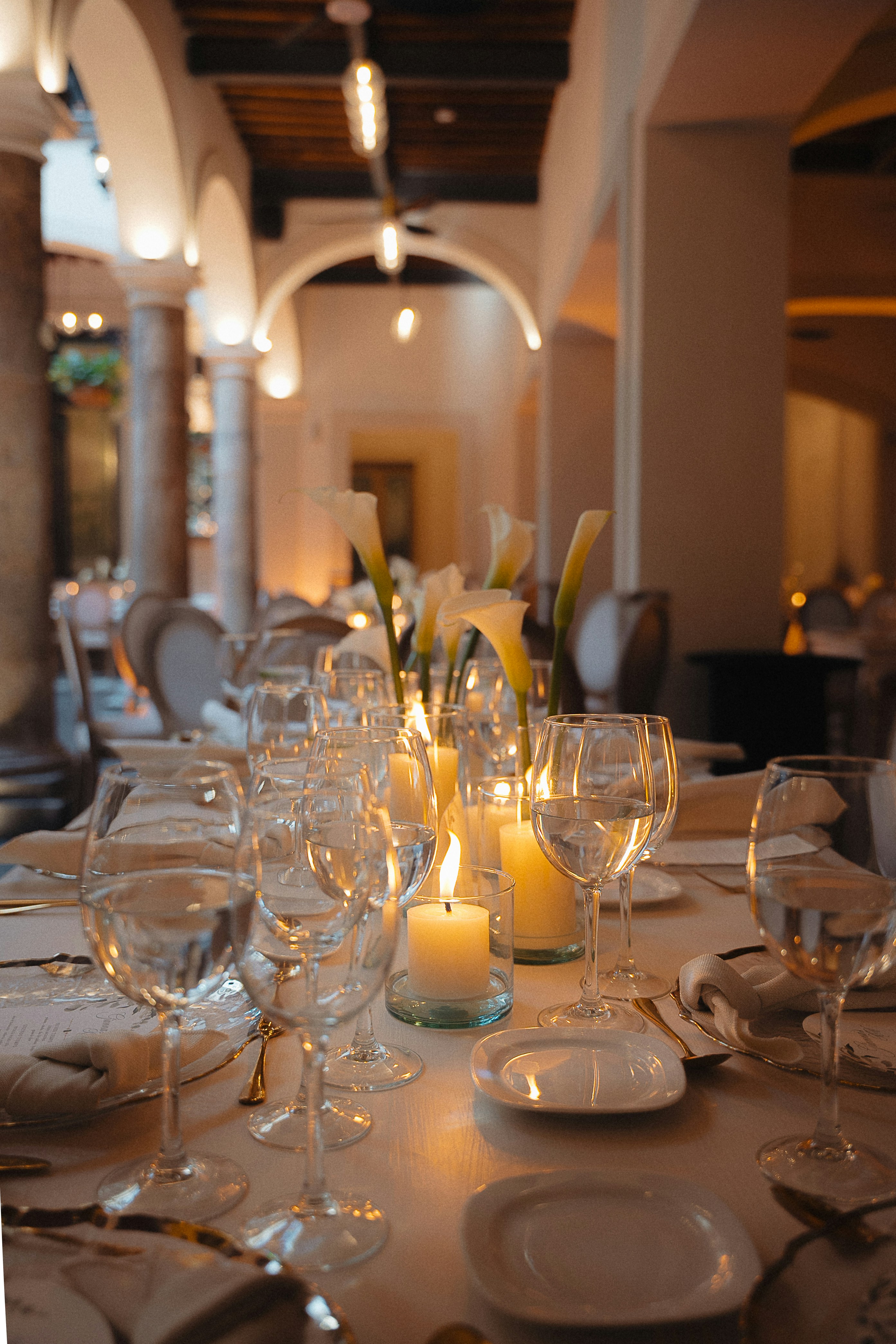 Candlelit table setting with glassware and floral centerpiece in an elegant dining hall.
