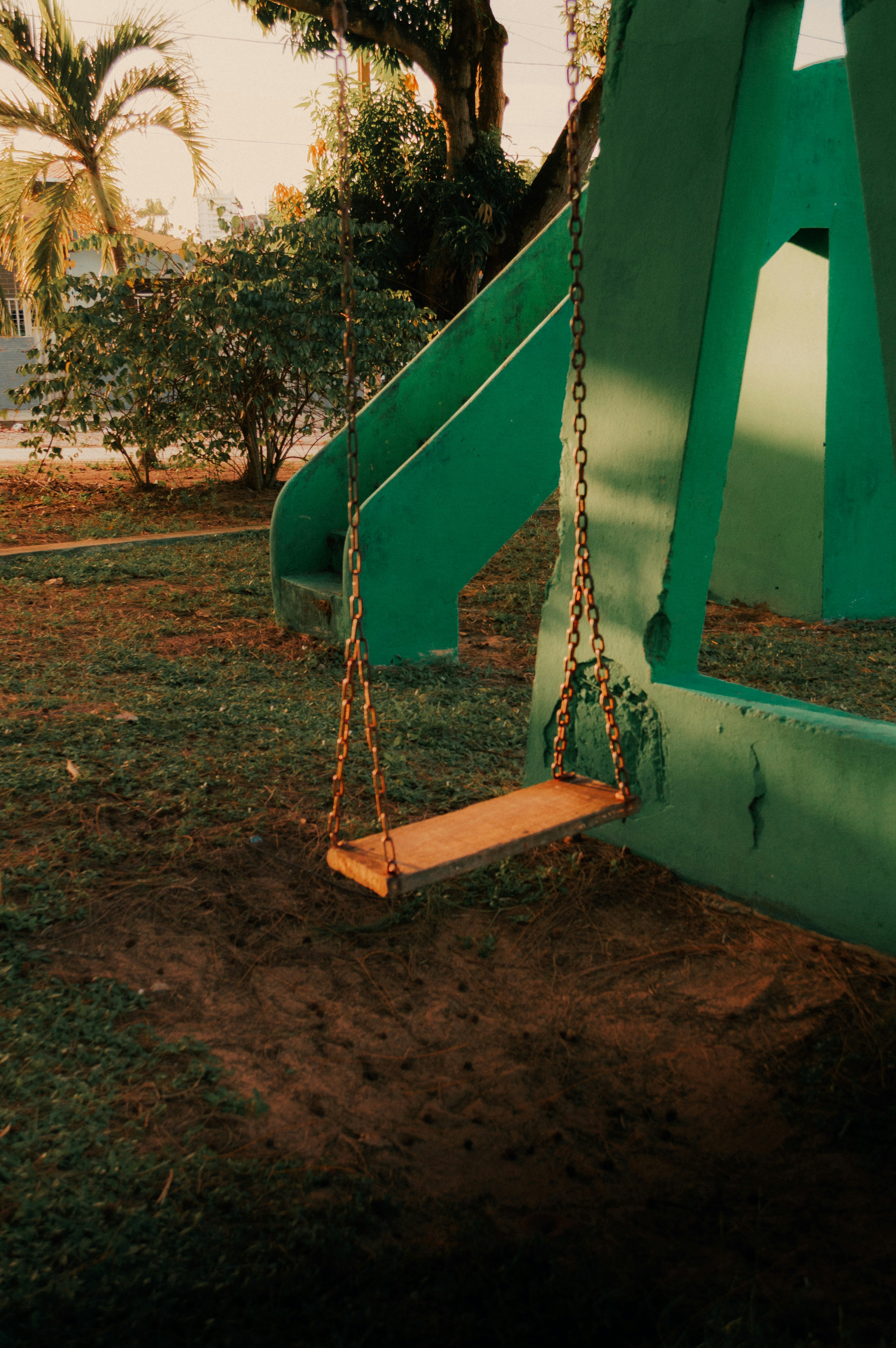 A solitary wooden swing in a sunlit green playground.