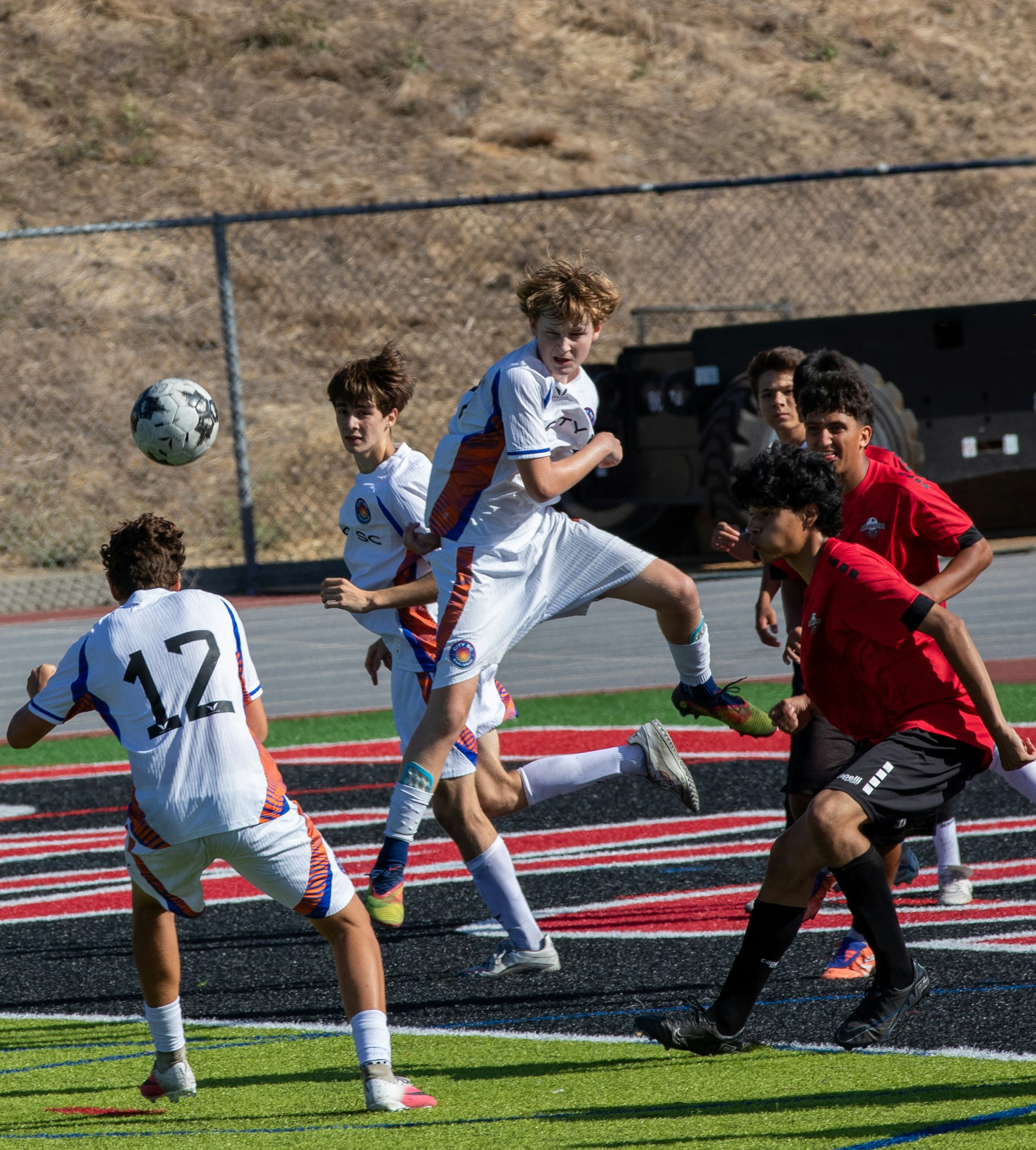 Midair Challenge: A White Jersey Targets the Ball Amid Soccer Scramble