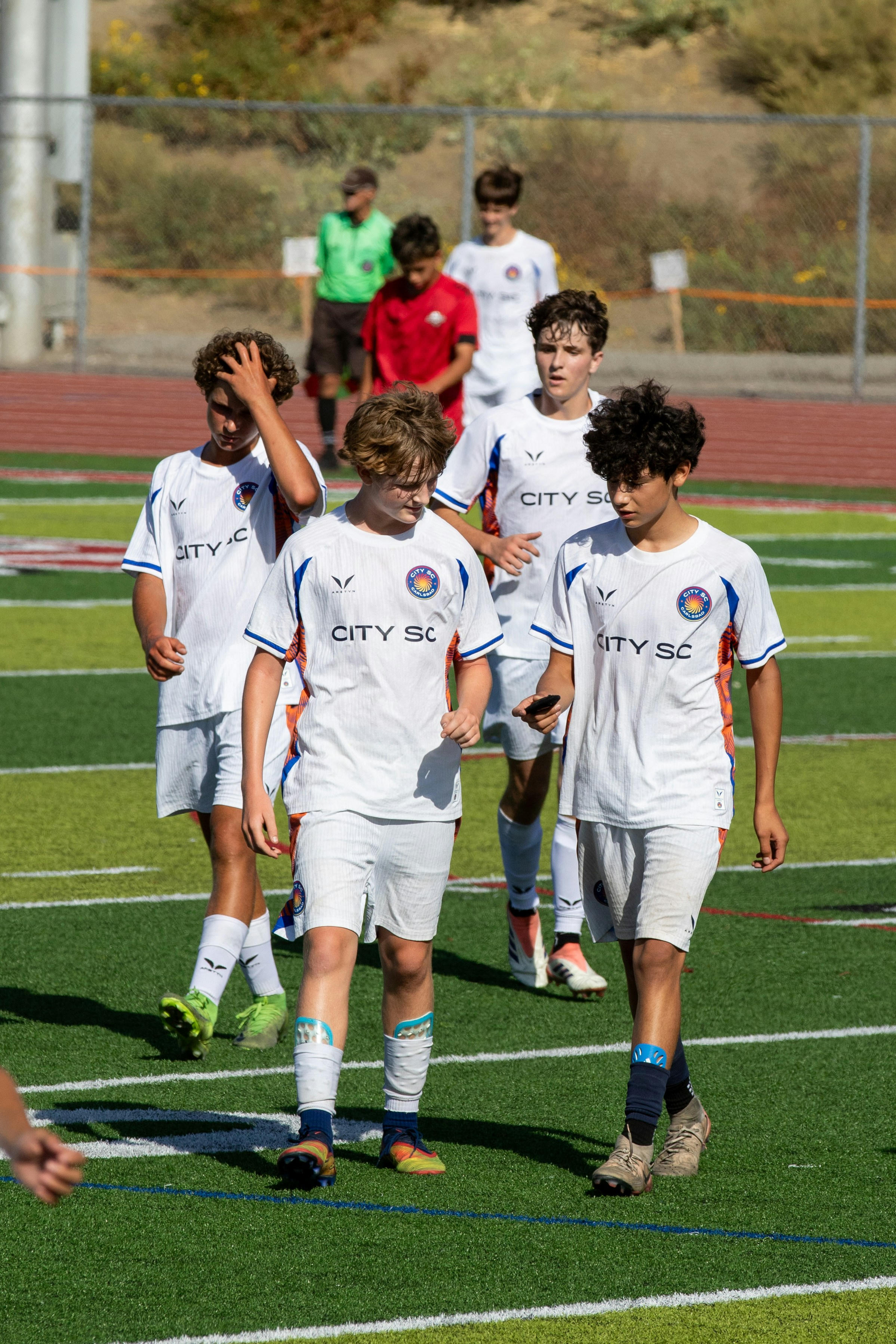 White-clad teammates share a quiet moment after a game on a sunlit field